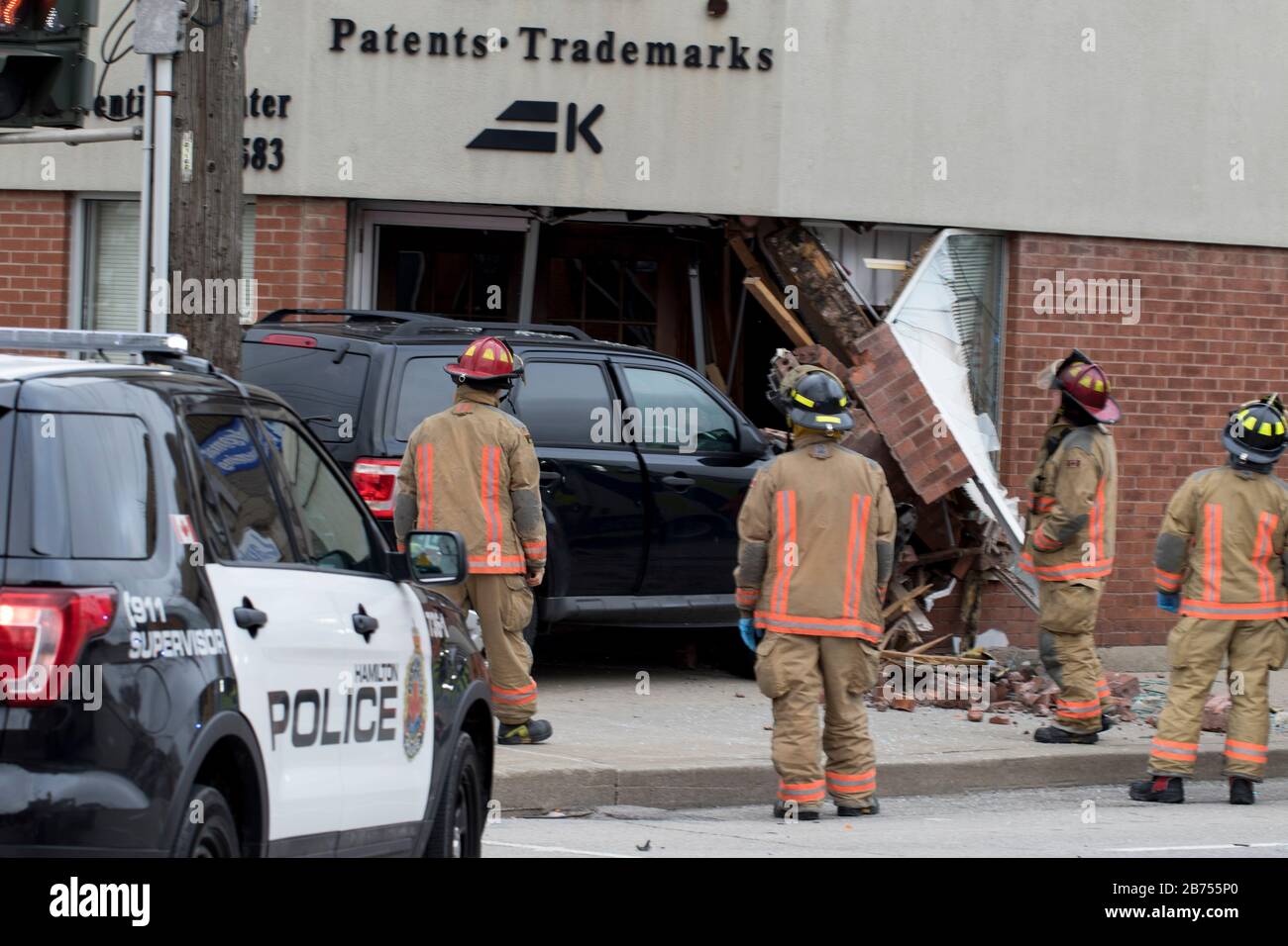 Firemen inspecting car crash into brick building. Building and car ...