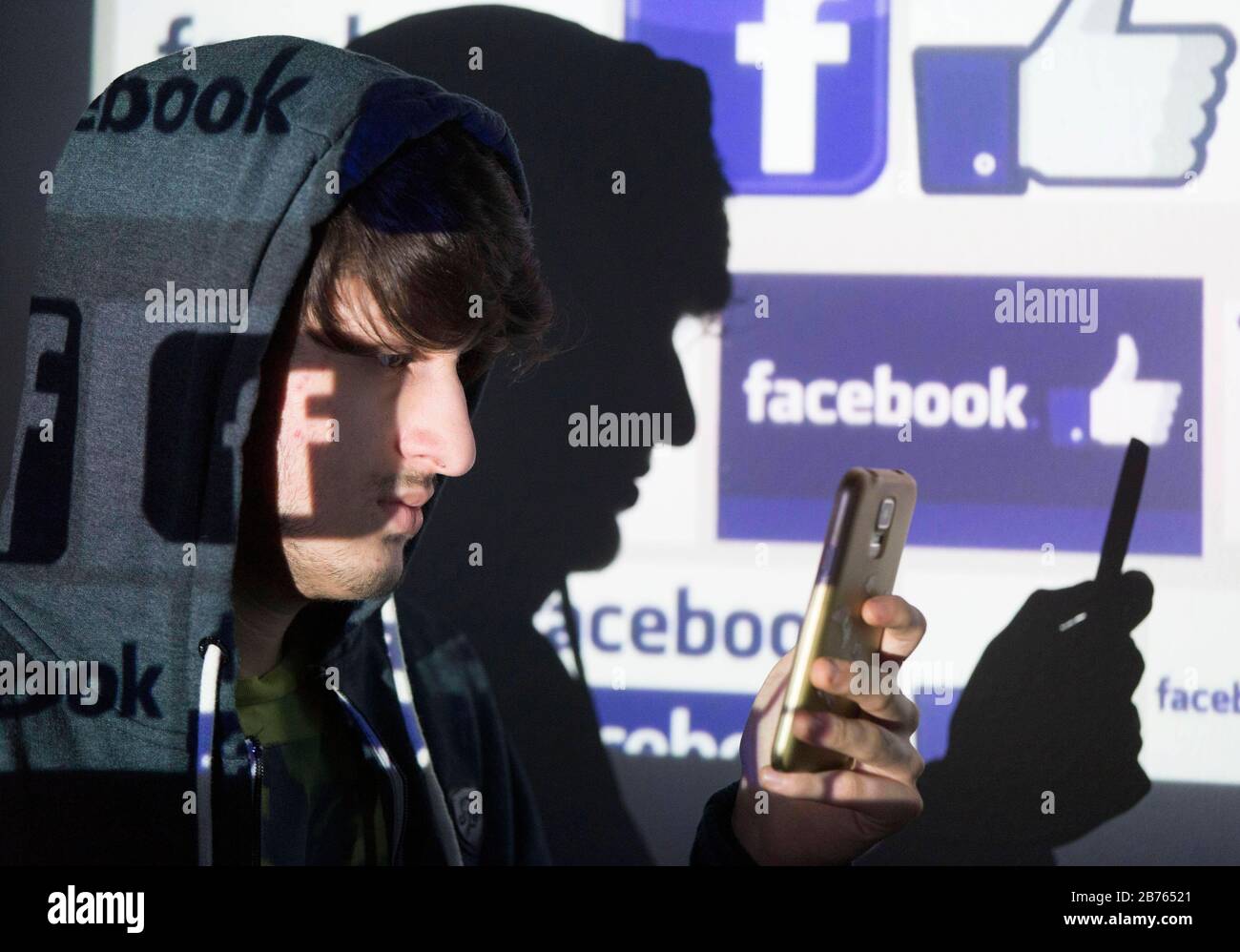 The silhouette of a young man with a smartphone in his hand can be seen ...