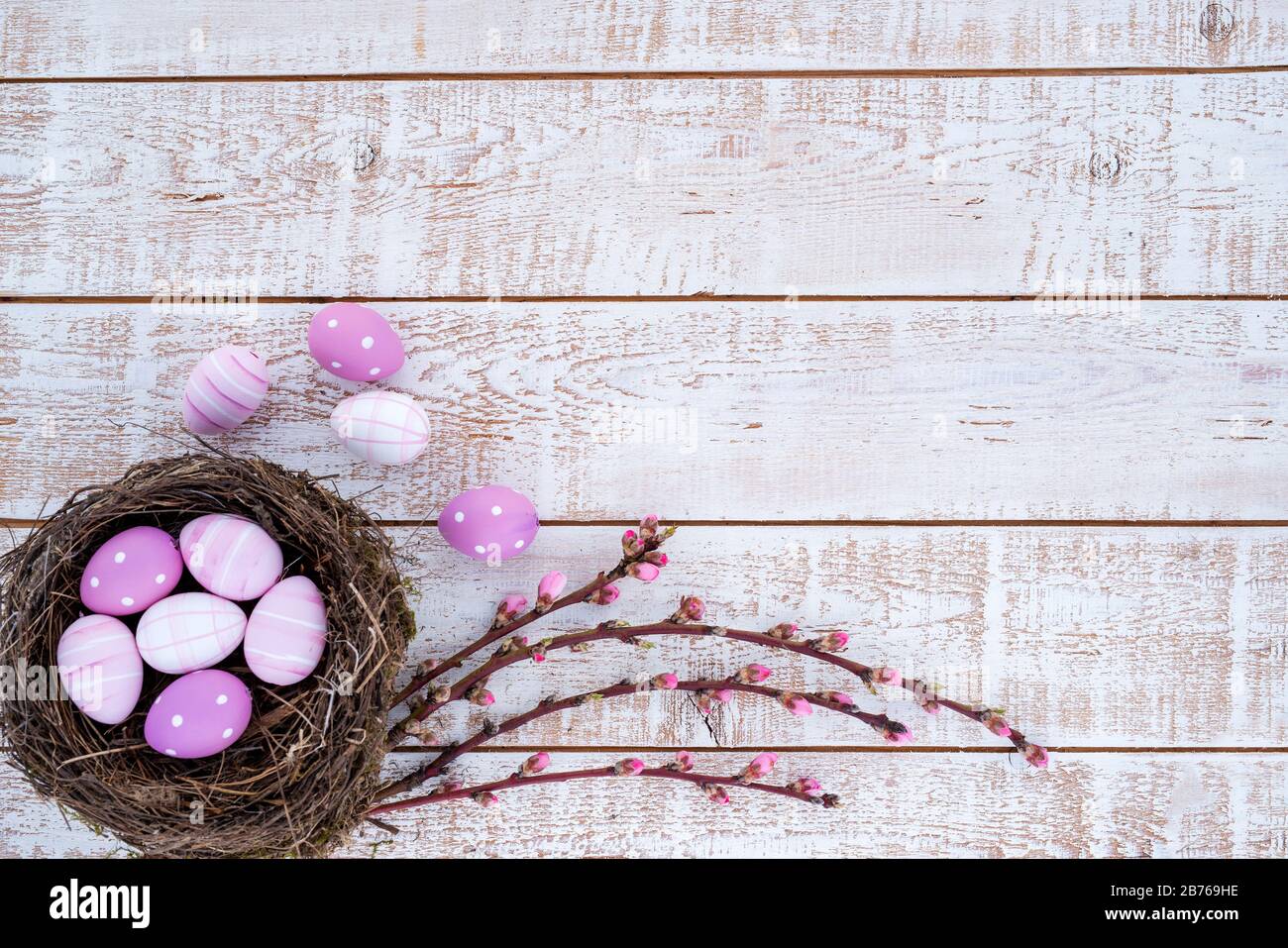 Easter background with colorful eggs in a nest over white wooden rustic ...