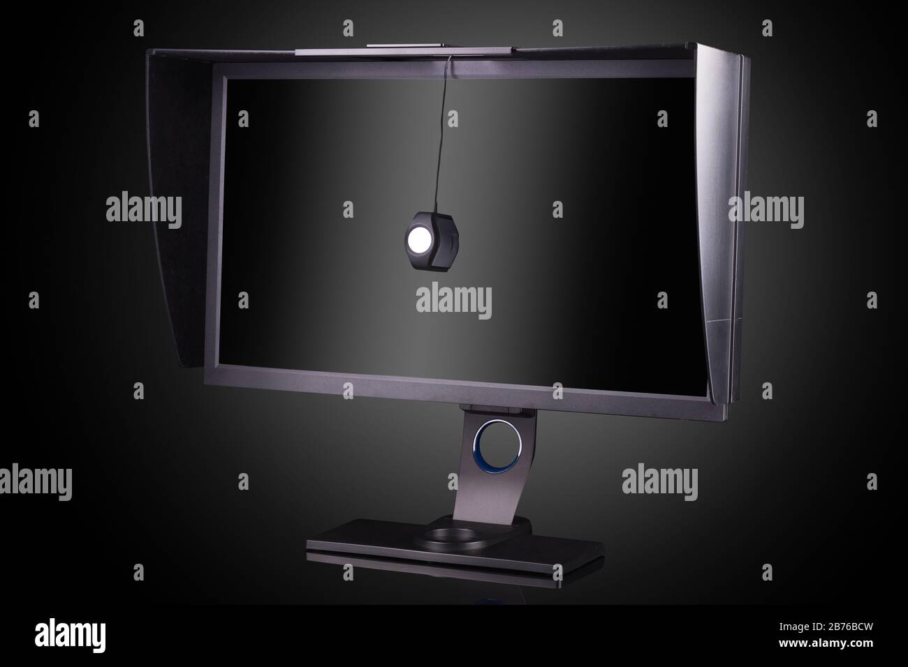 Professional monitor with shading hood and calibrator isolated on black ...