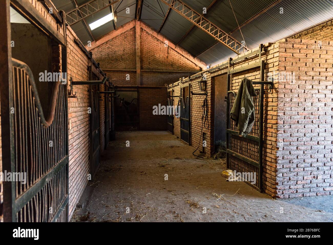 Inside a bricks stable with a lot of horses stals and one of them open ...