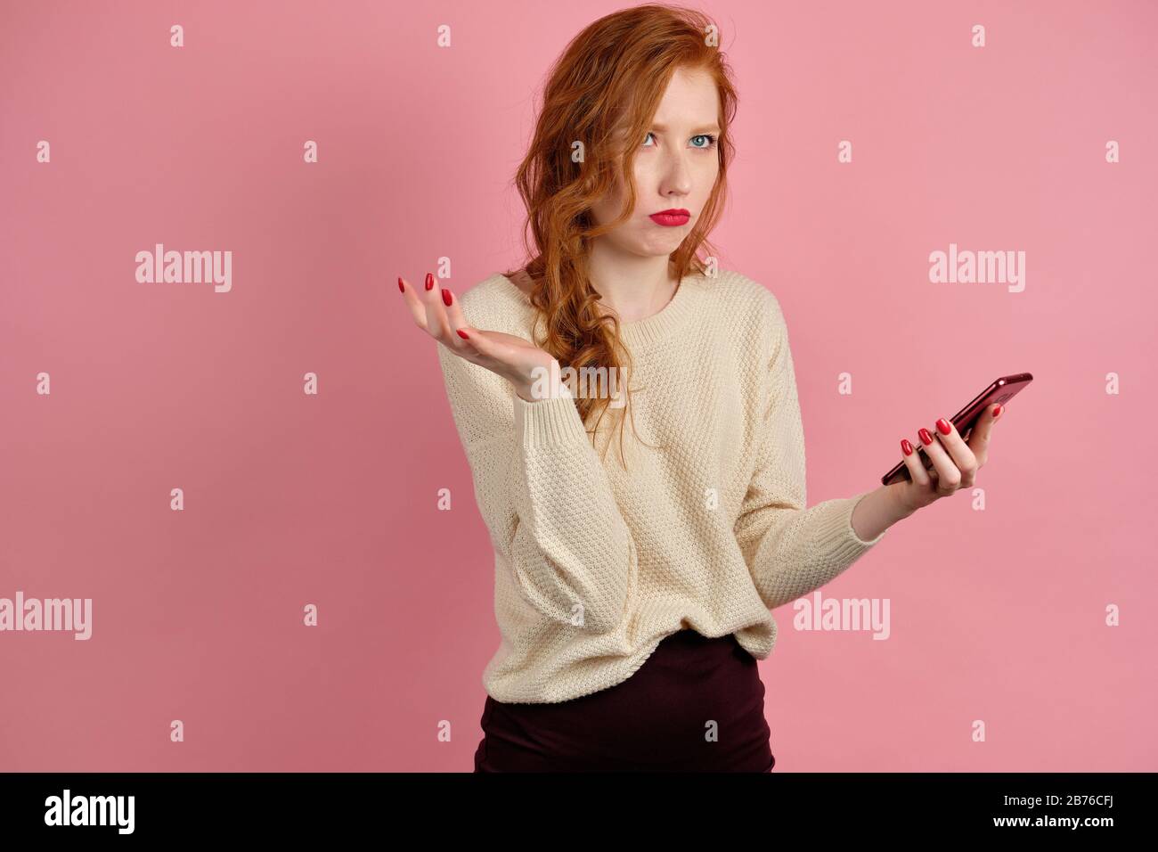 A red-haired girl with red lipstick on a pink background with a phone ...