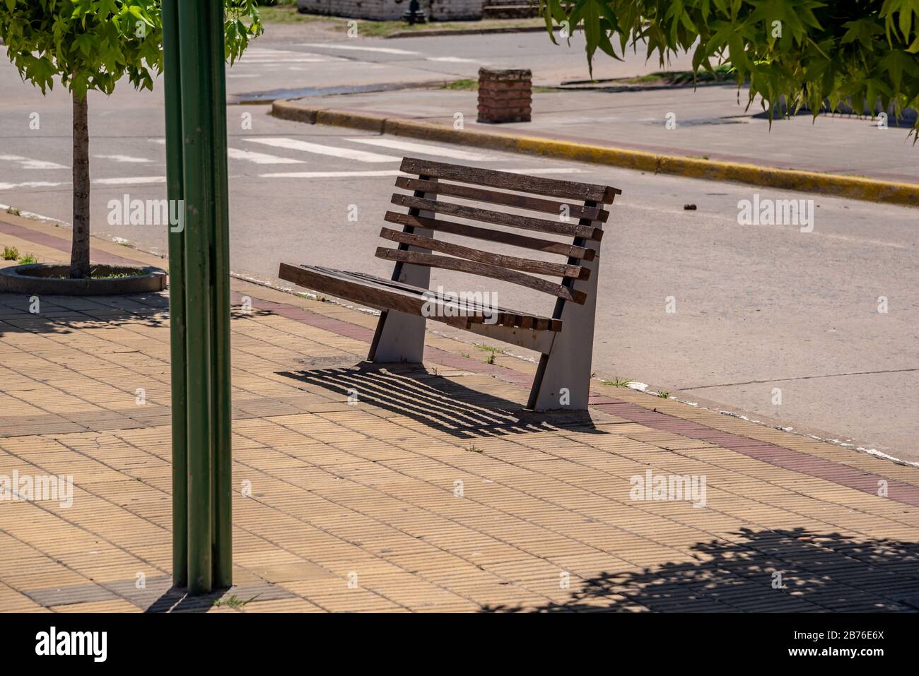 Wooden bench in a sidewalk with the view of a street and a pedestrian ...