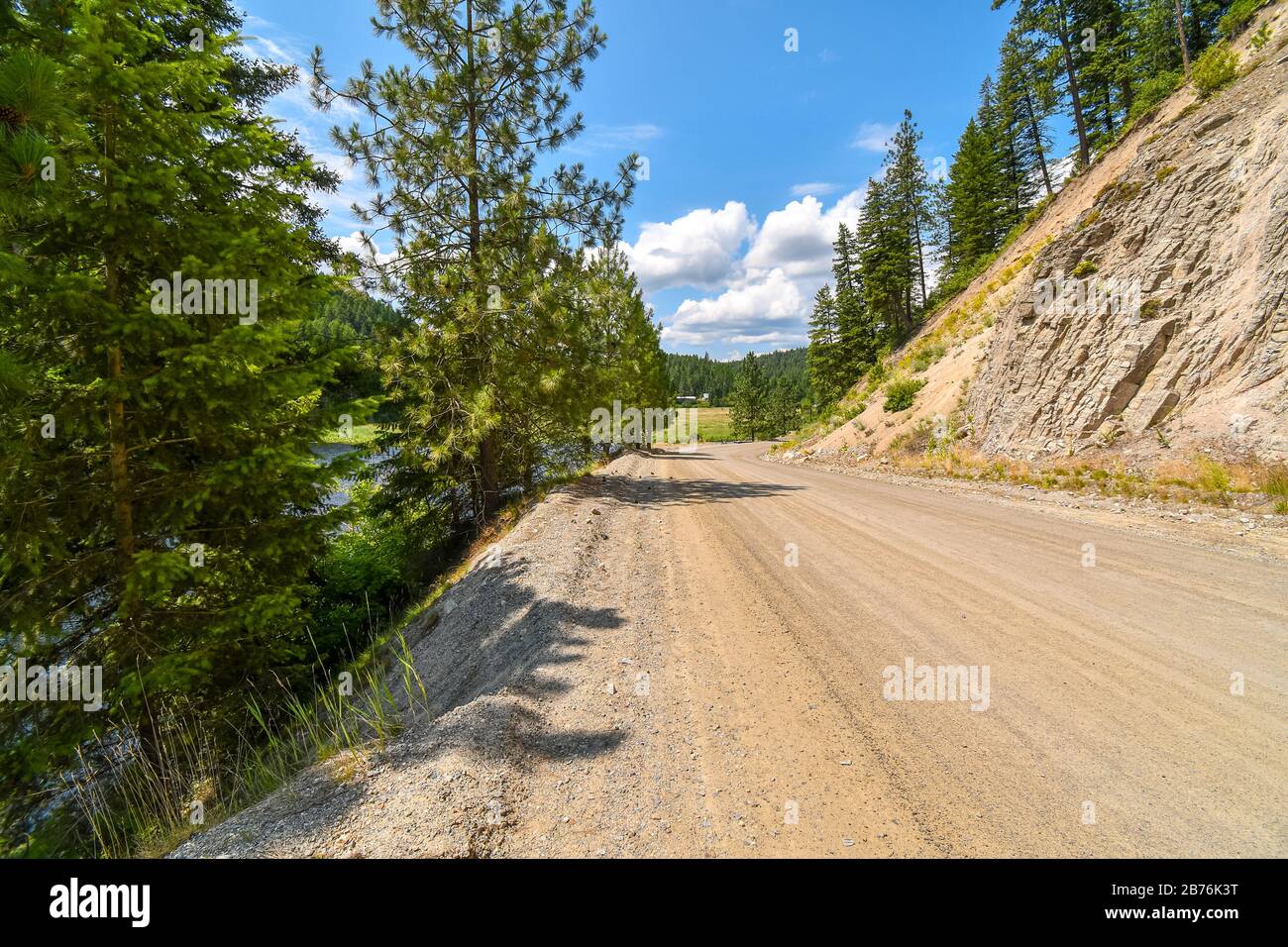 A rural dirt road with a steep mountain on one side and a ravine on the ...