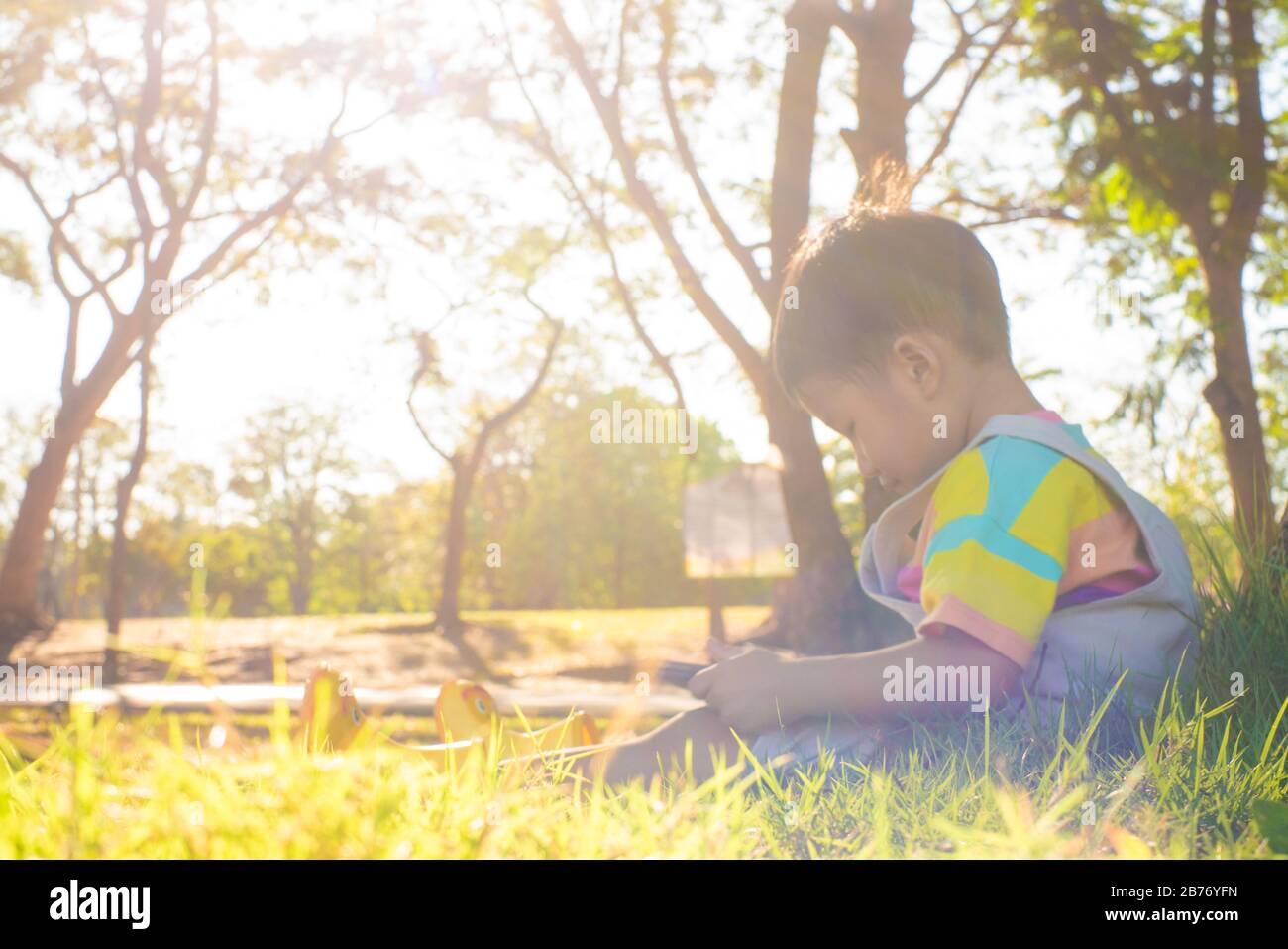 Adorable asian boy sitting under tree use tablet computer technology ...