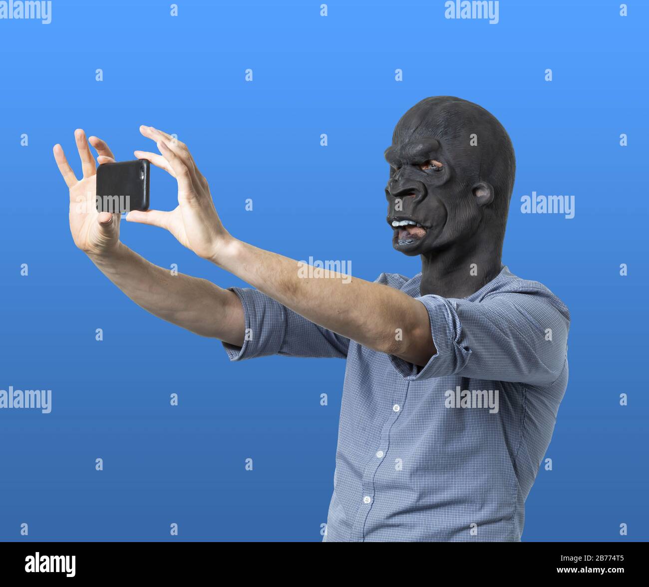 Male in a black angry mask taking a selfie with a phone on a blue ...