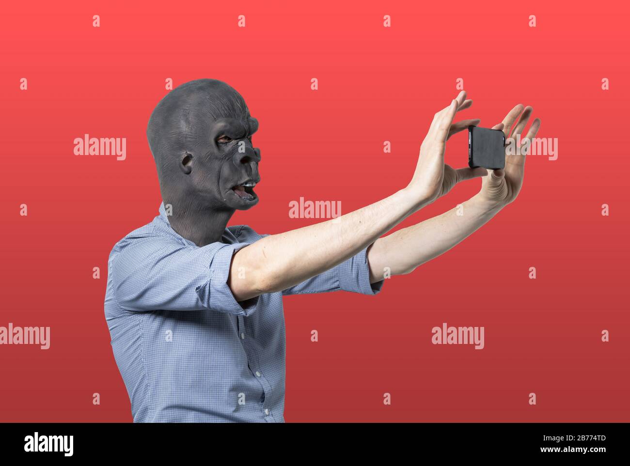 Male in a black angry mask taking a selfie with a phone on a red ...