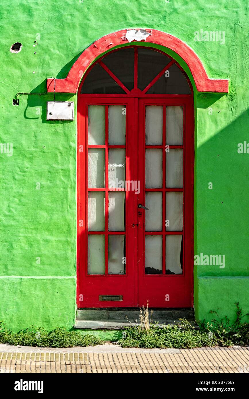 Old red door with rusted and cracked paint in a green wall with grass ...