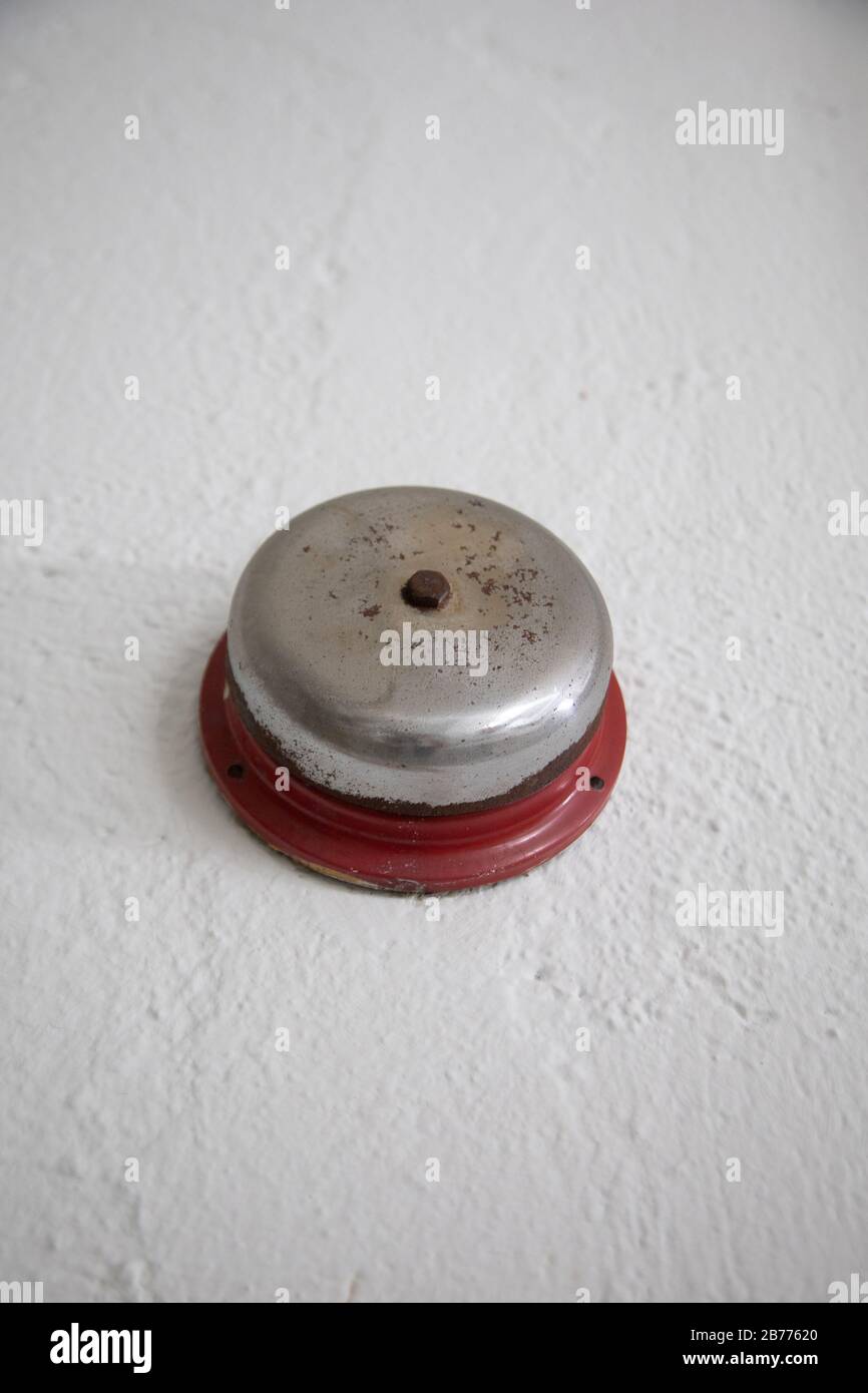 Closeup of an old rusty school bell on a white wall under the lights ...