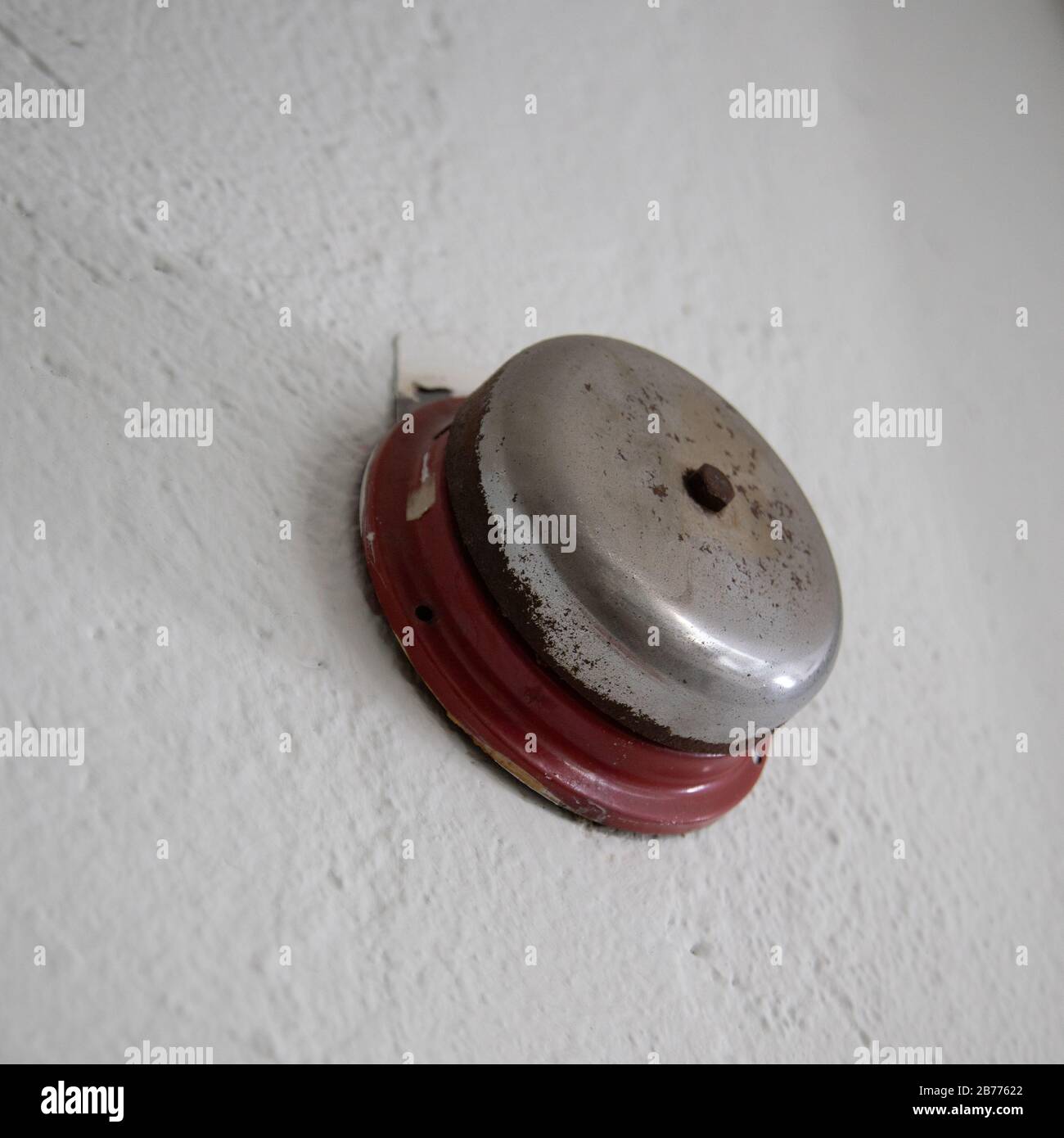 Closeup of an old rusty school bell on a white wall under the lights ...