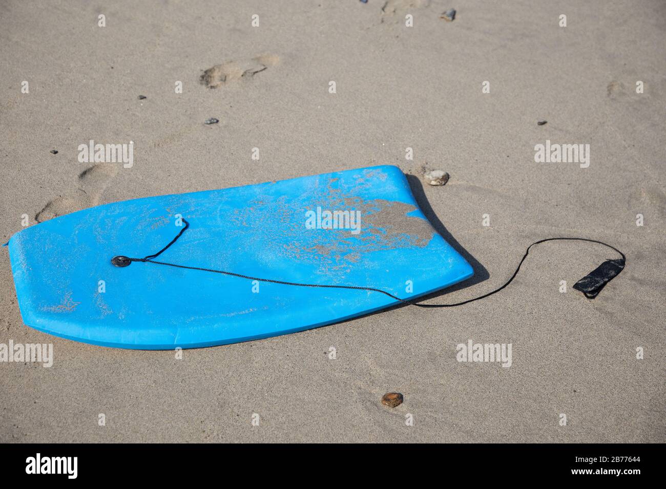 Closeup of a blue bodyboard on the sand in a beach under the sunlight ...