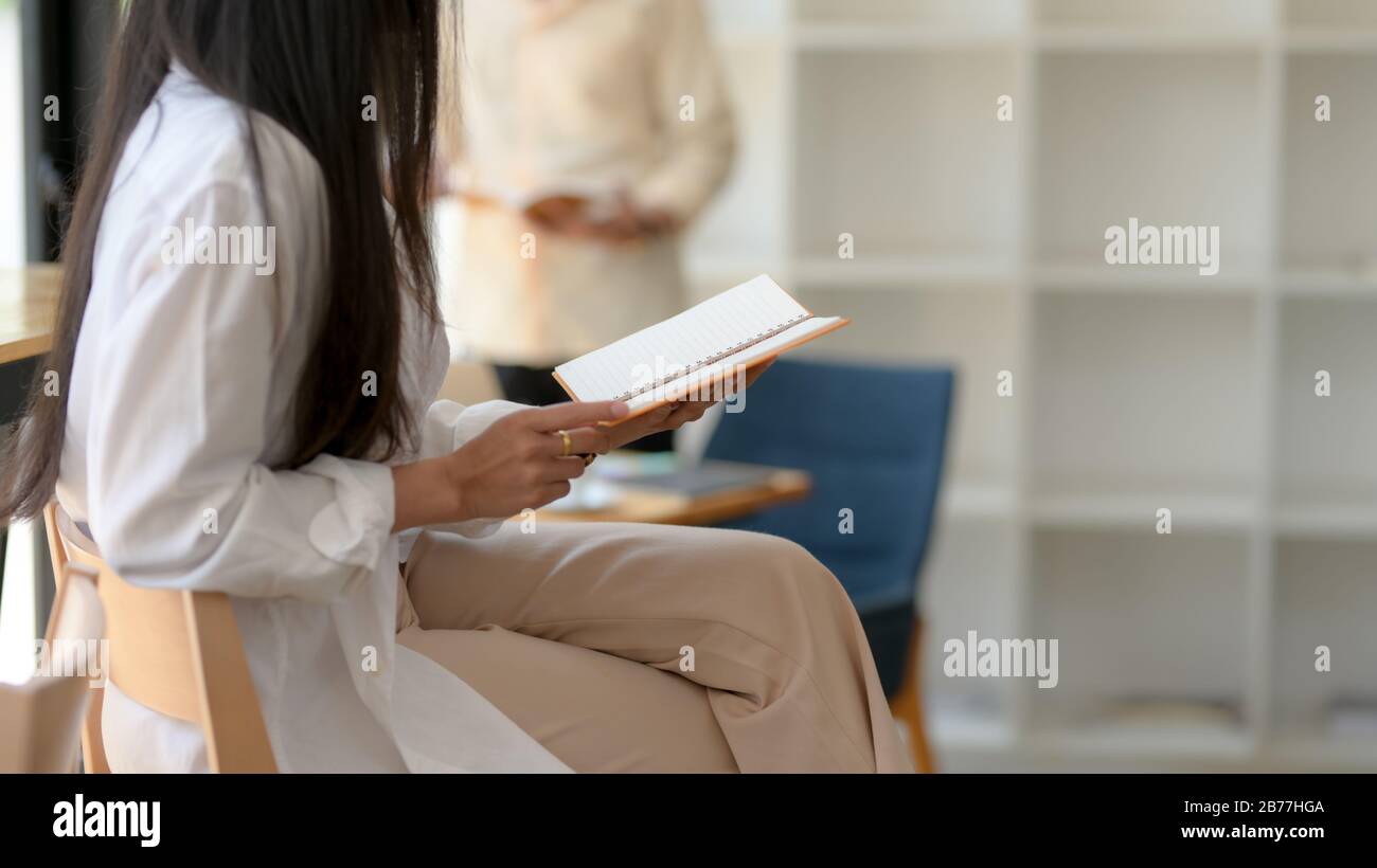 Side view of female university student reading a book while sitting on ...