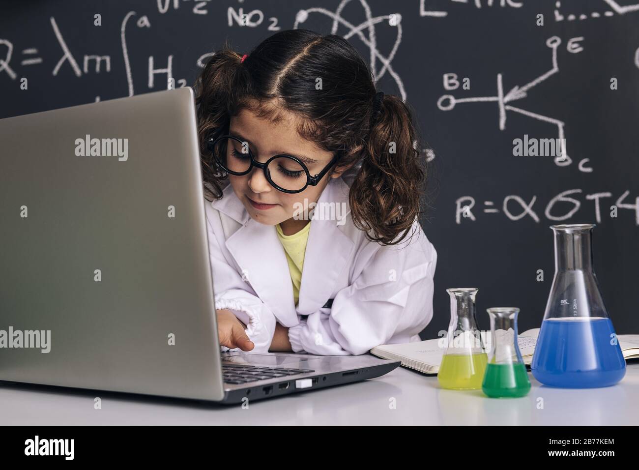 little scientist girl with glasses in lab coat typing on the computer ...