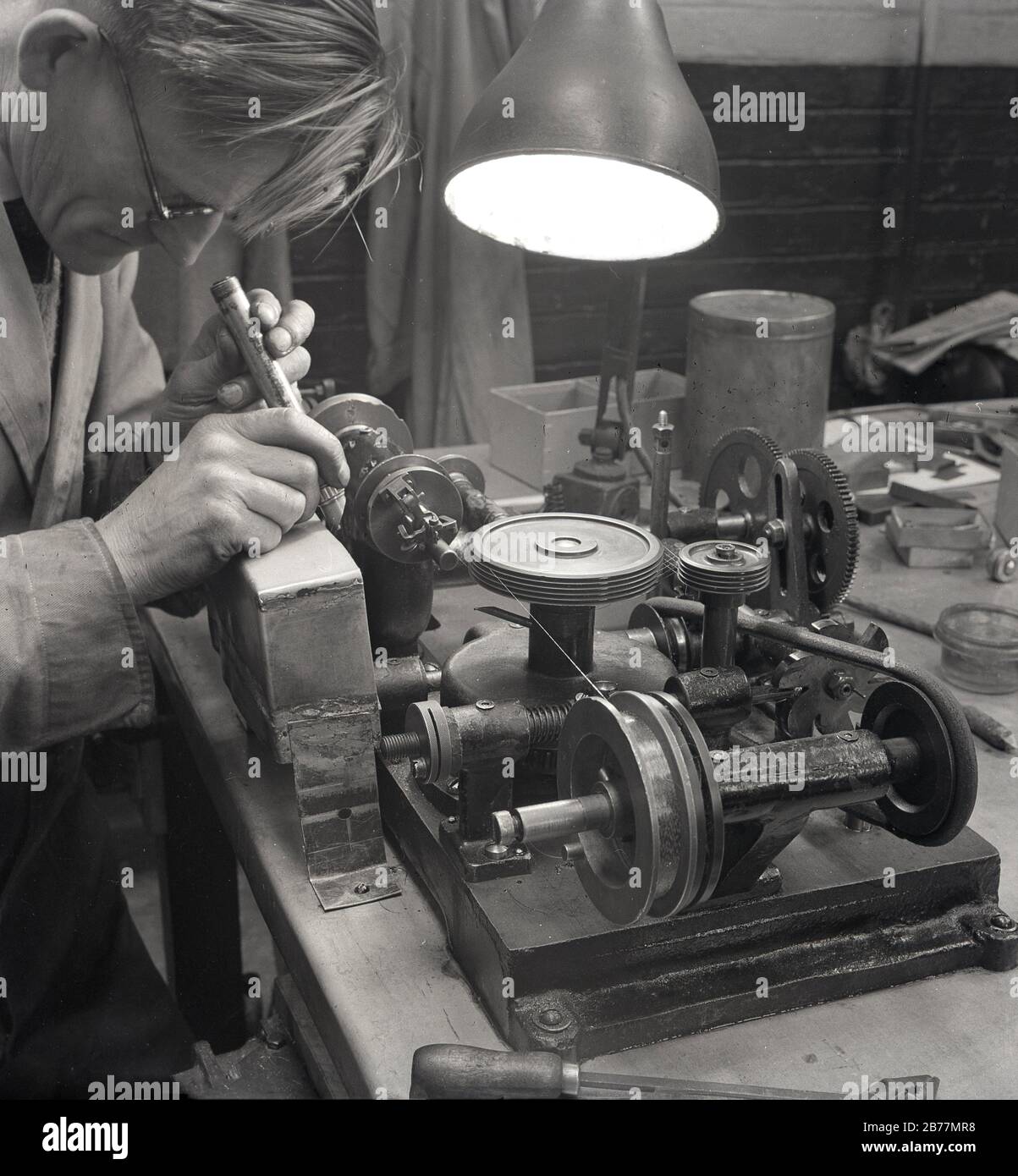 1950s, historical, male worker at a workbench using a small machine ...