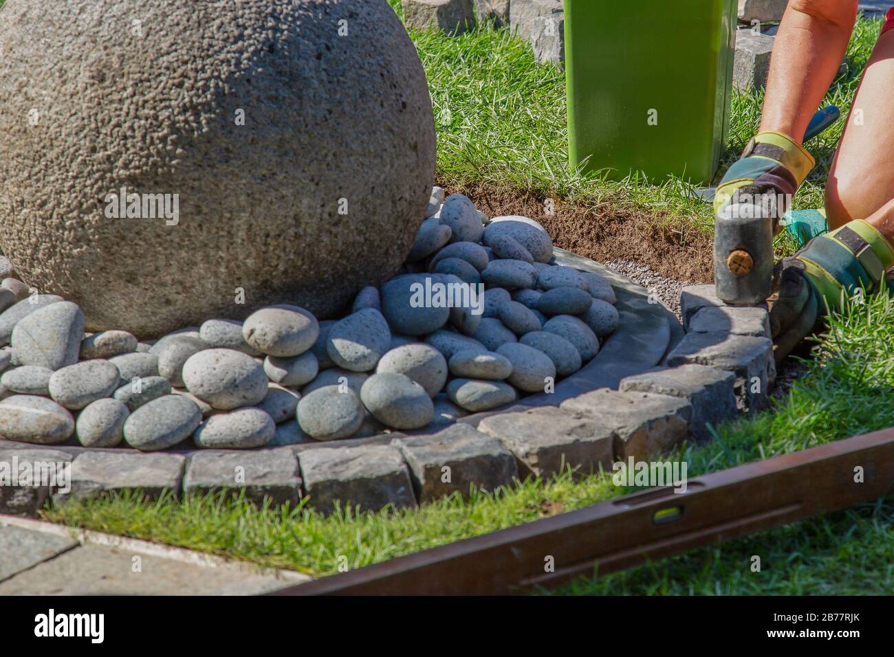 Parts of a hobby worker with work gloves arranging basalt cobblestones ...