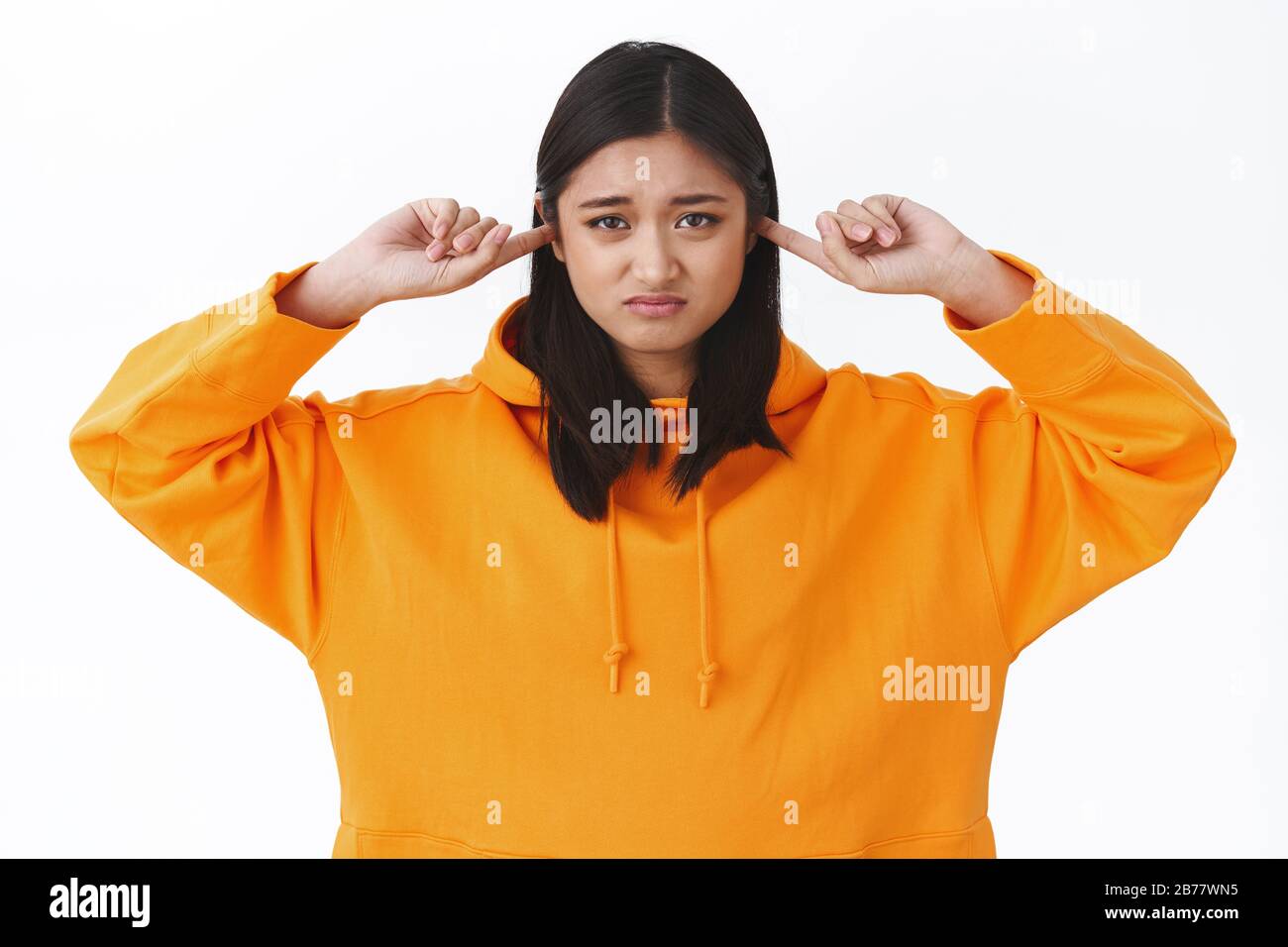 Waist-up portrait gloomy and sulking young asian woman in orange hoodie, grimacing and pursing ...