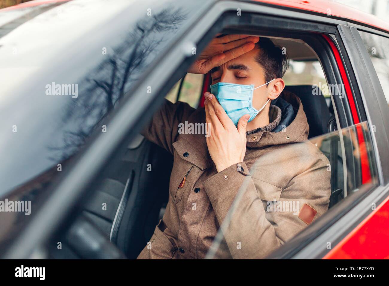 Ill man sitting in car wearing protective mask feeling sick having flu ...