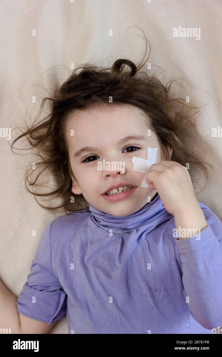 Little kid girl after accident laying down with adhesive palter on face ...