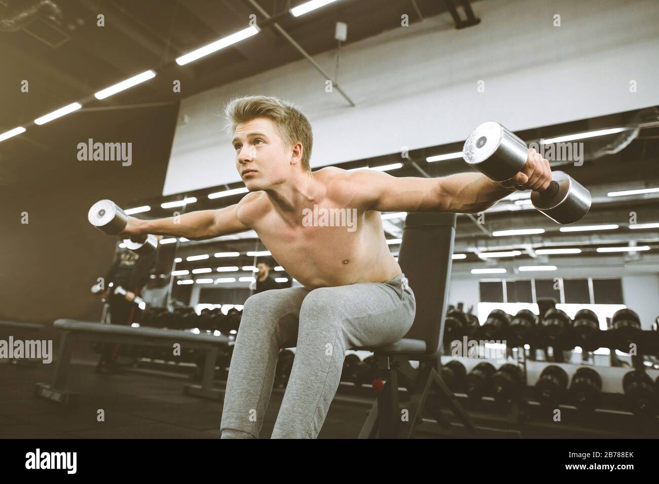 Concentrated sporty guy during workout in gym with dumbbells. Lifts ...