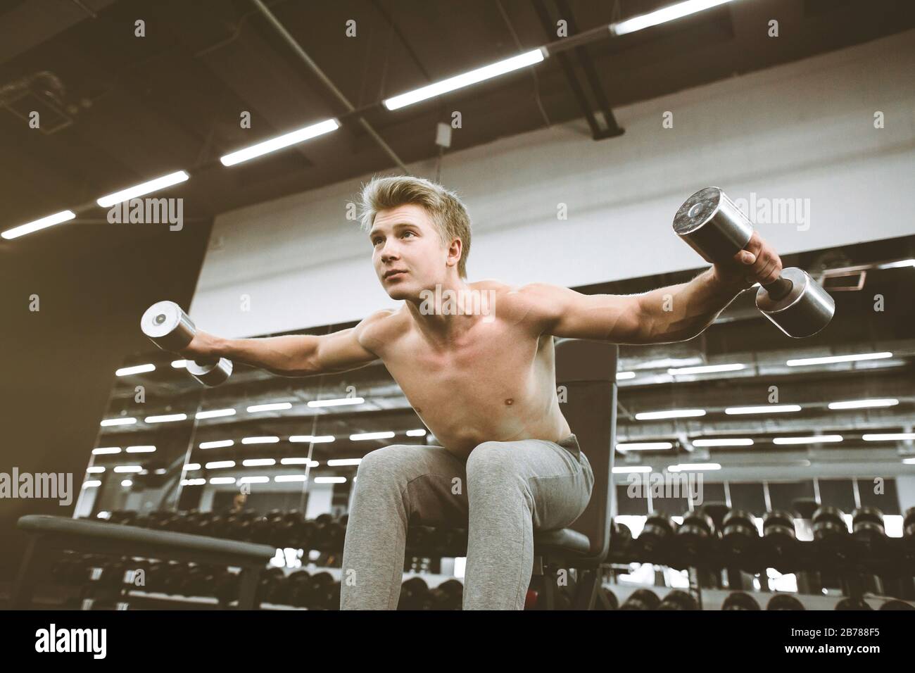 Concentrated sporty guy during workout in gym with dumbbells. Lifts ...