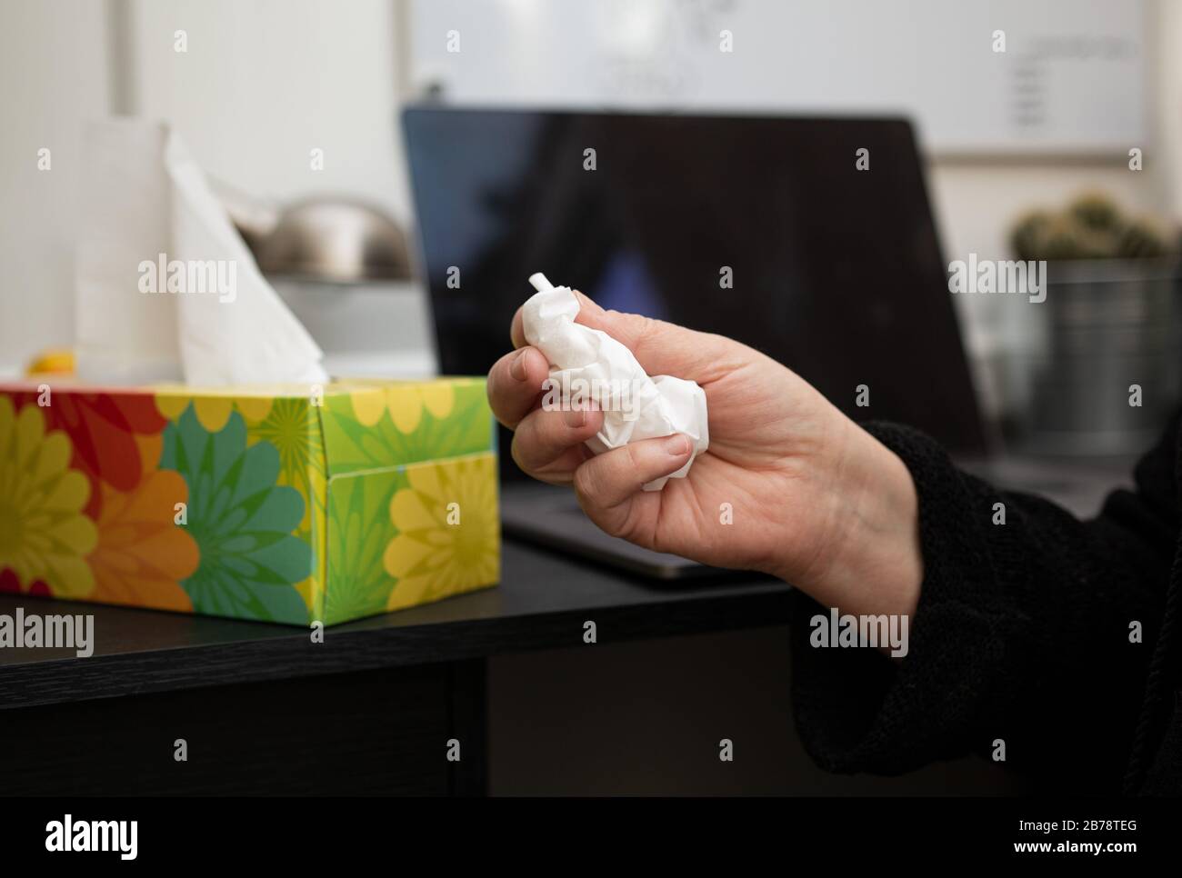 hand holding a disposable tissue, next to the tissue box in an office ...