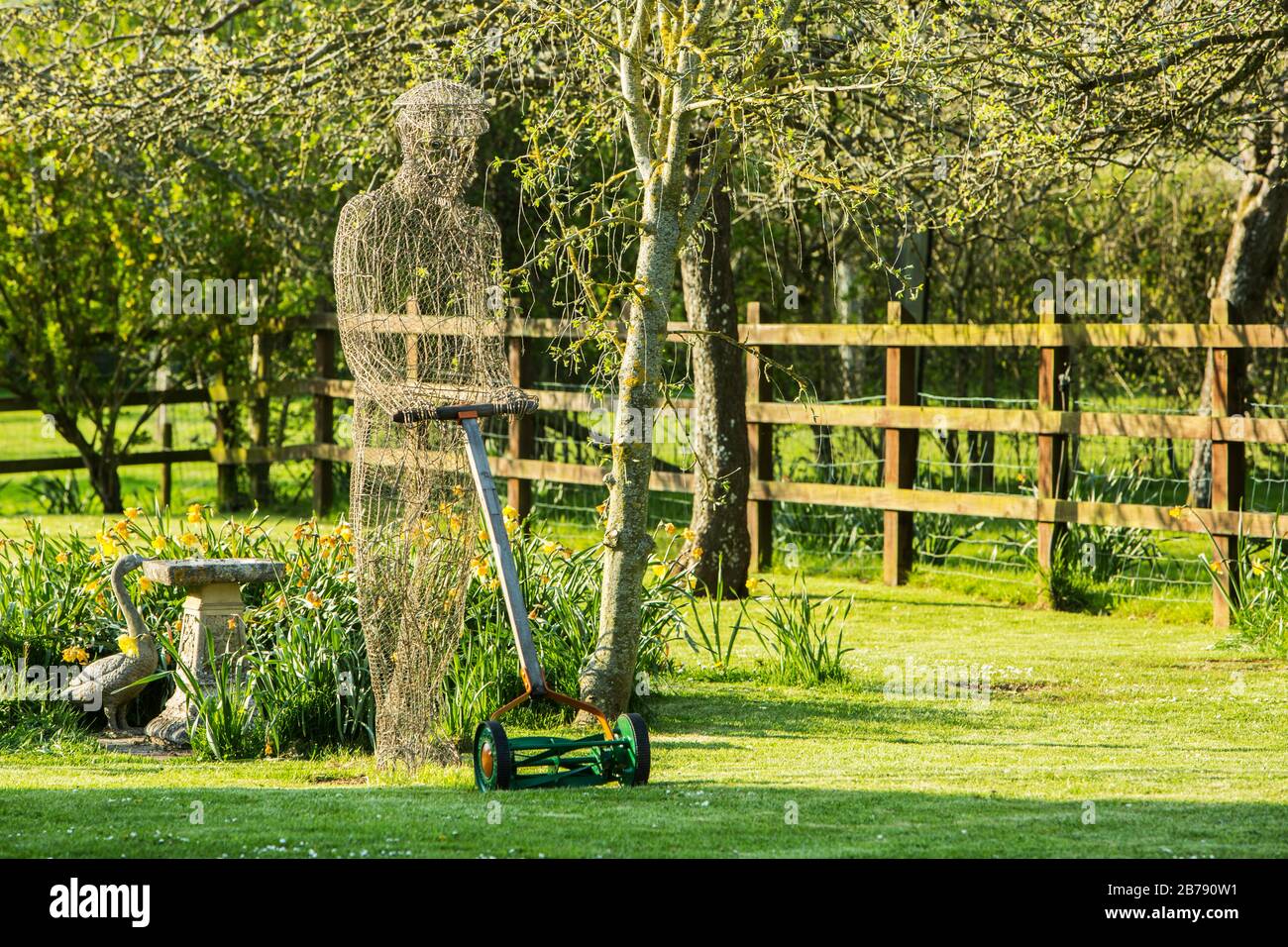 Wire statue of a man gardener mowing the lawn in a spring garden ...