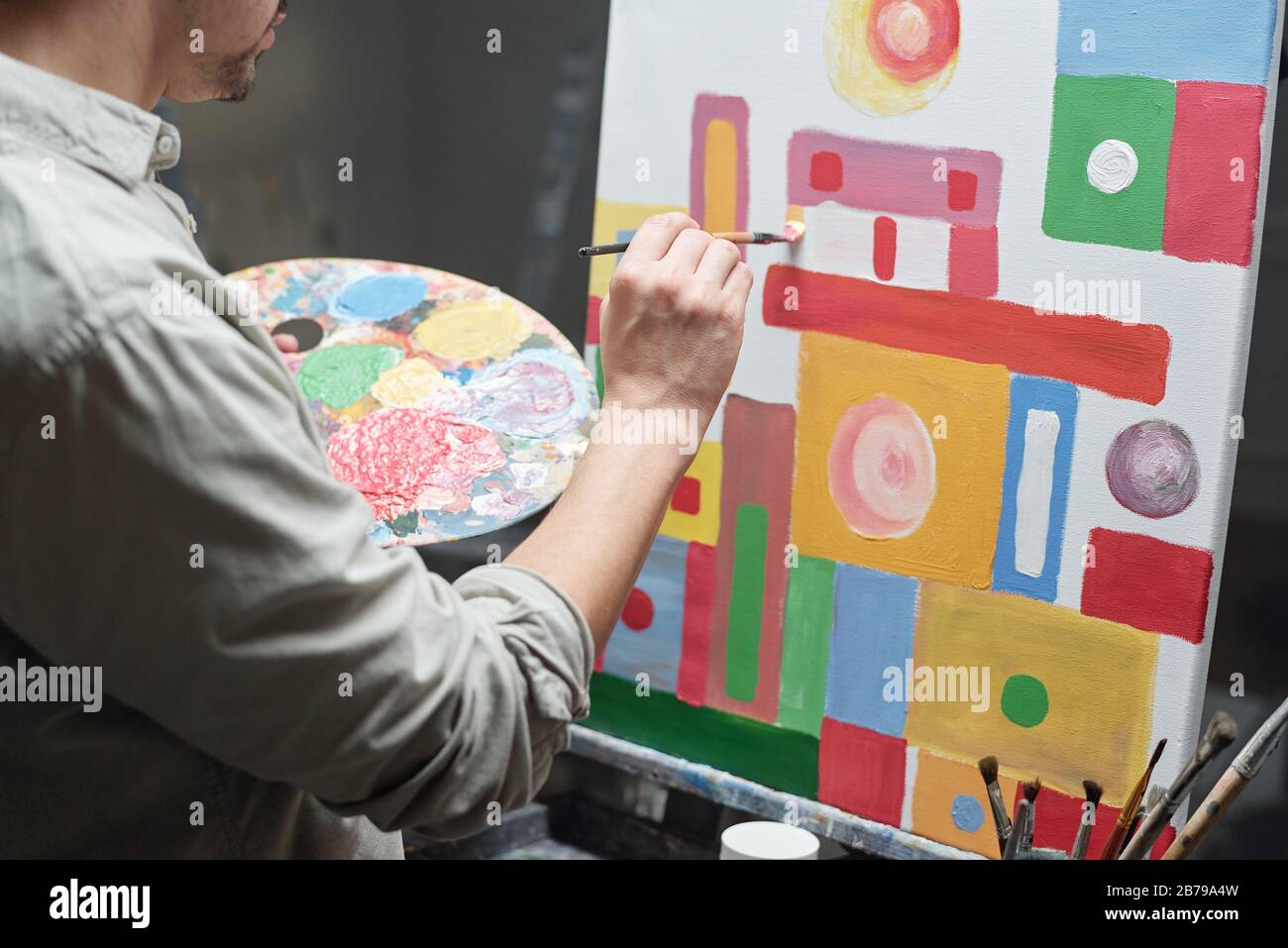 Young male artist with color palette and paintbrush working over ...