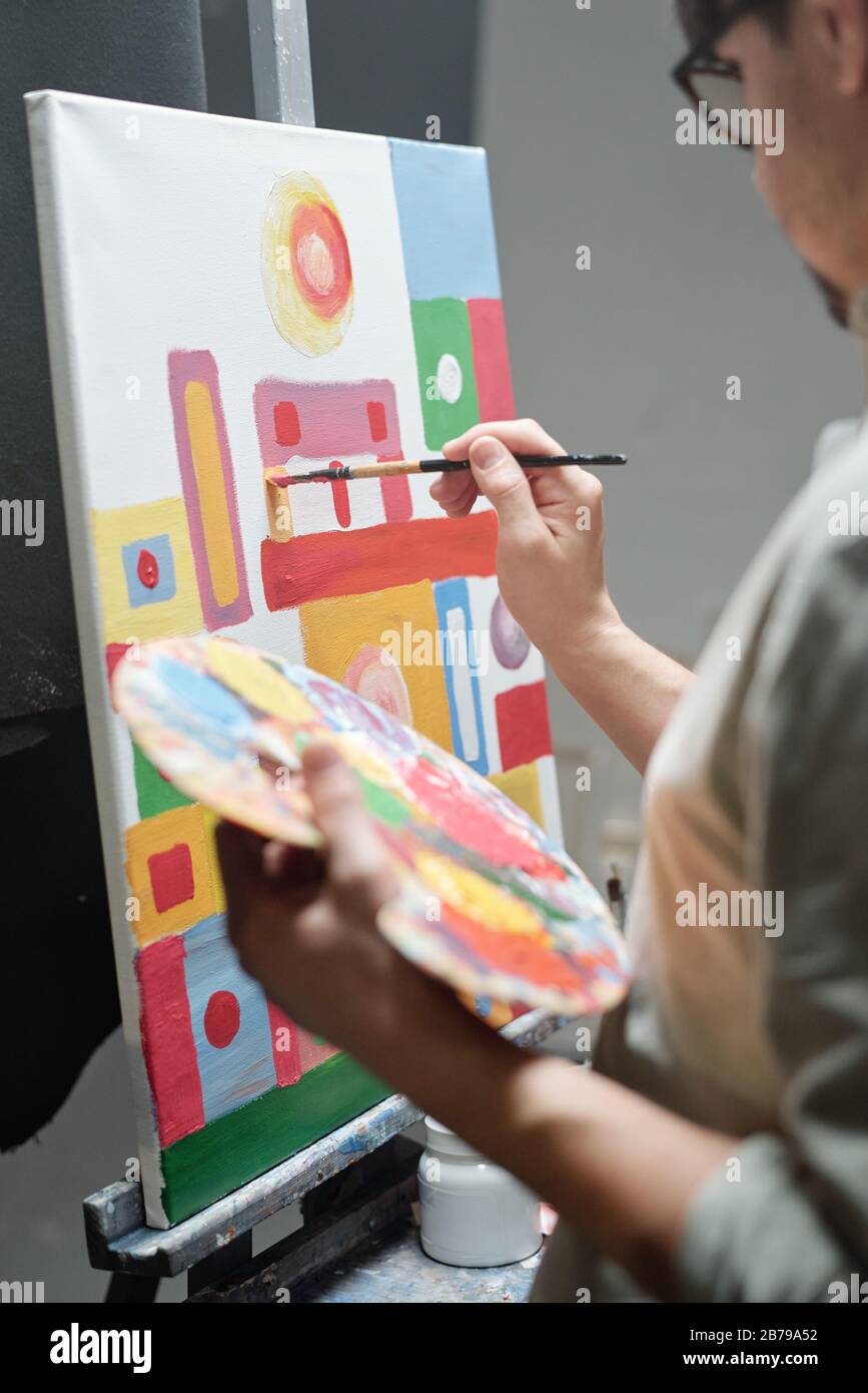 Hand of young artist holding color palette while using paintbrush ...