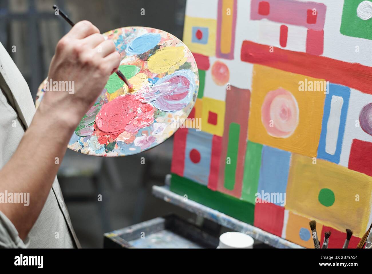 Hand of male artist with paintbrush and palette mixing colors while ...