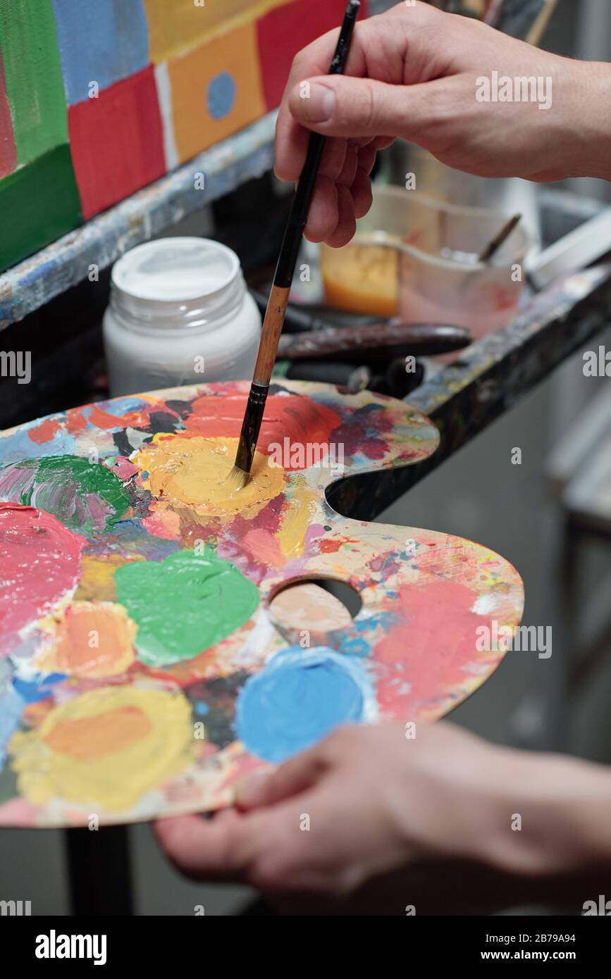 Hand of young professional painter mixing colors on palette while ...