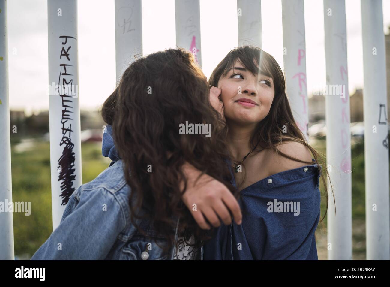 Girl kissing her friend in front of a white metal fence Stock Photo - Alamy