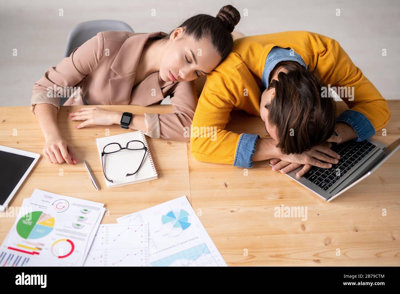 Two young exhausted brokers napping by desk - man lying on laptop ...