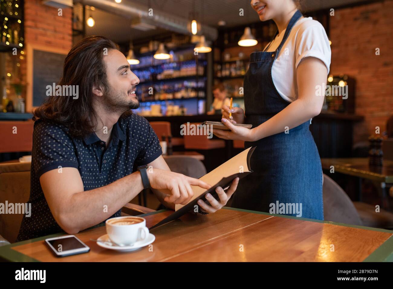 Happy young man pointing at menu while making order to waitress ...