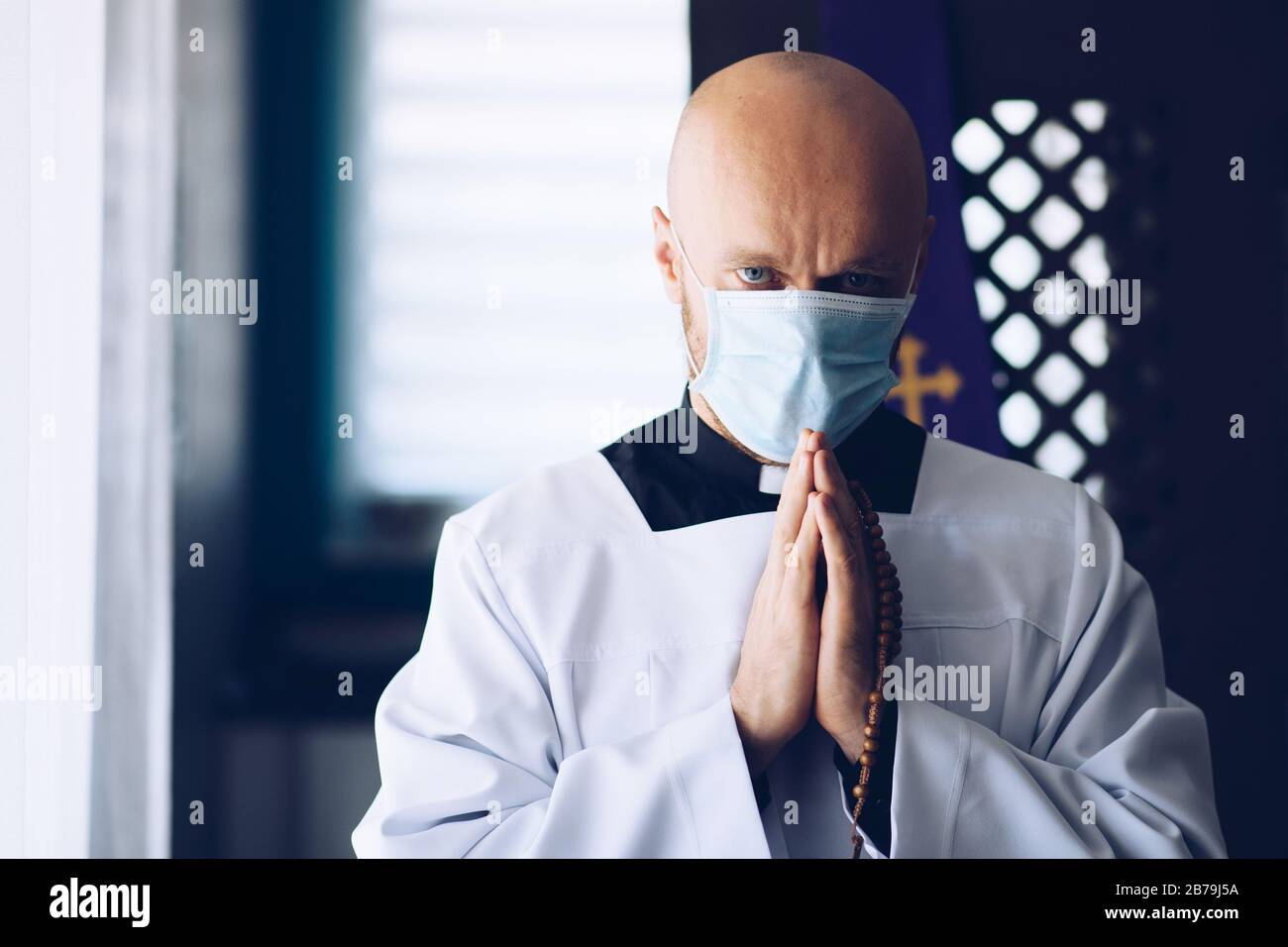 Man priest in medical mask praying with cross and rosary Stock Photo ...