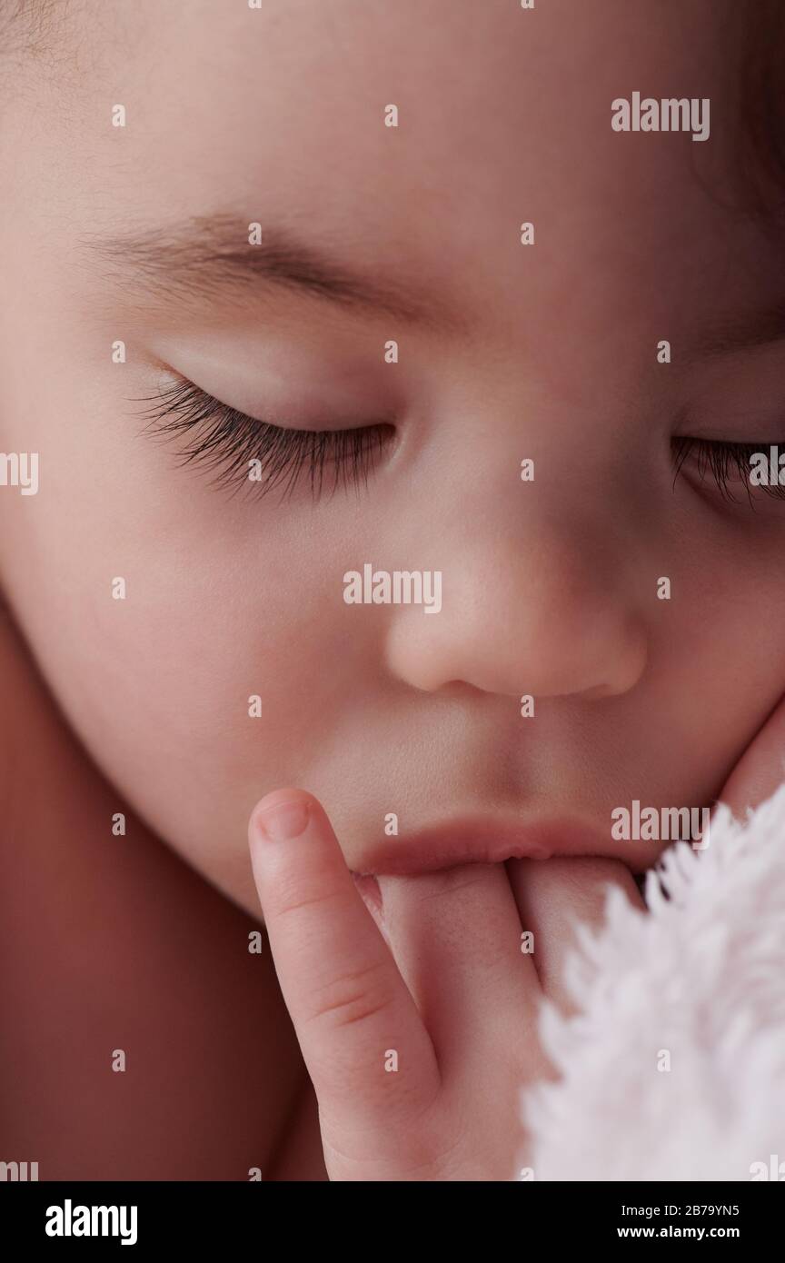 Newborn with fingers in mouth close up Stock Photo - Alamy