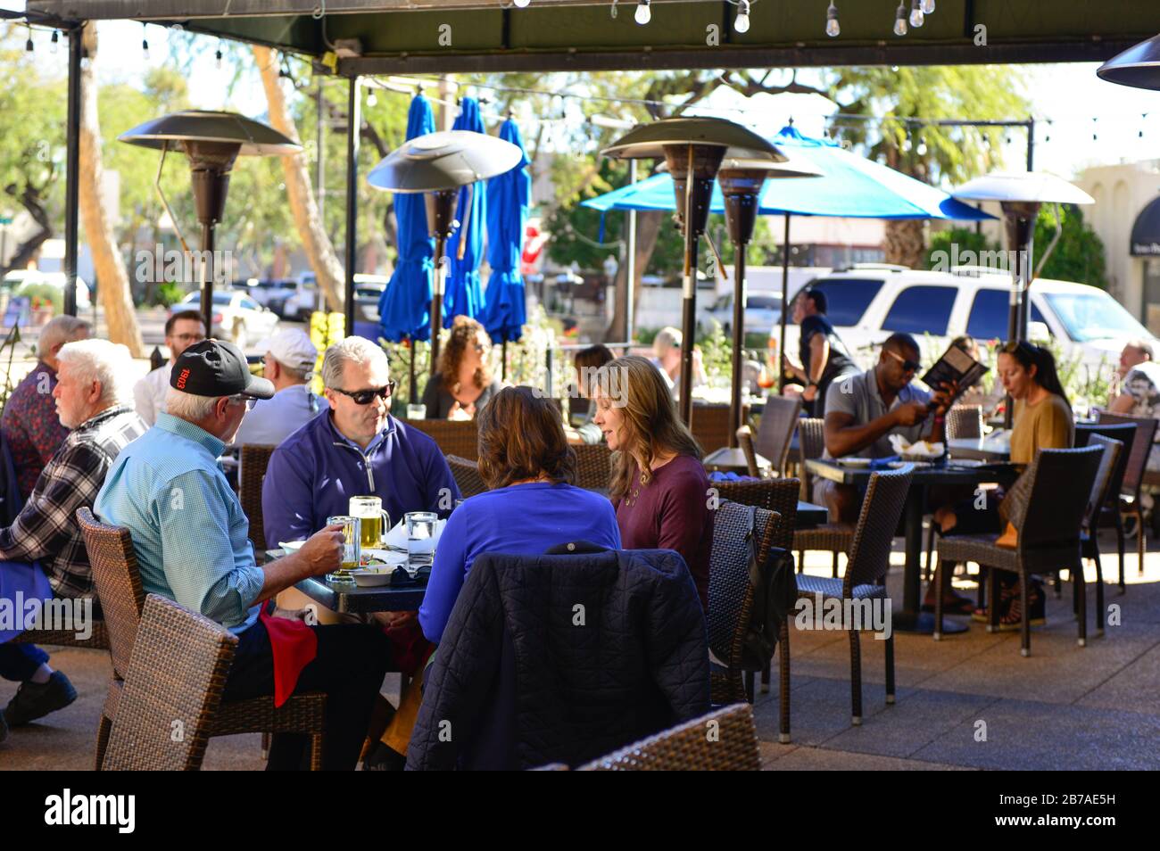 Groups of people drinking and eating at patio type tables outside of ...