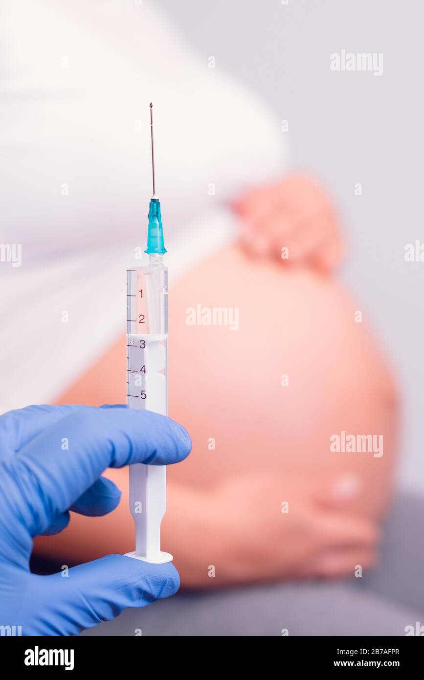 Pregnant woman having medicine injection. Hand with blue gloves holding ...
