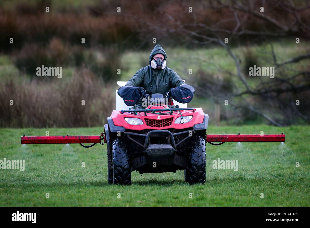 A farmer, in full protective gear, using a Suzuki quad to spray grass ...