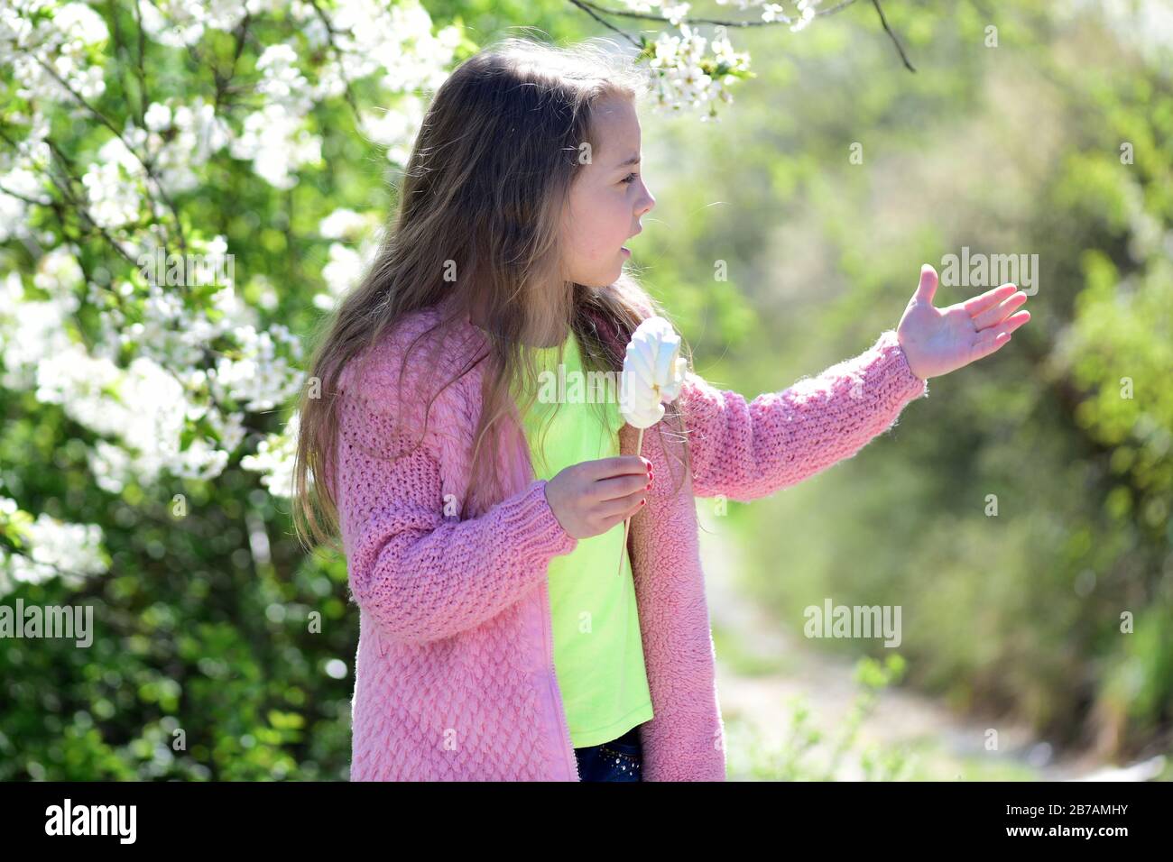 Kid in pink sweater holds lollipop. Schoolgirl walks outside near ...