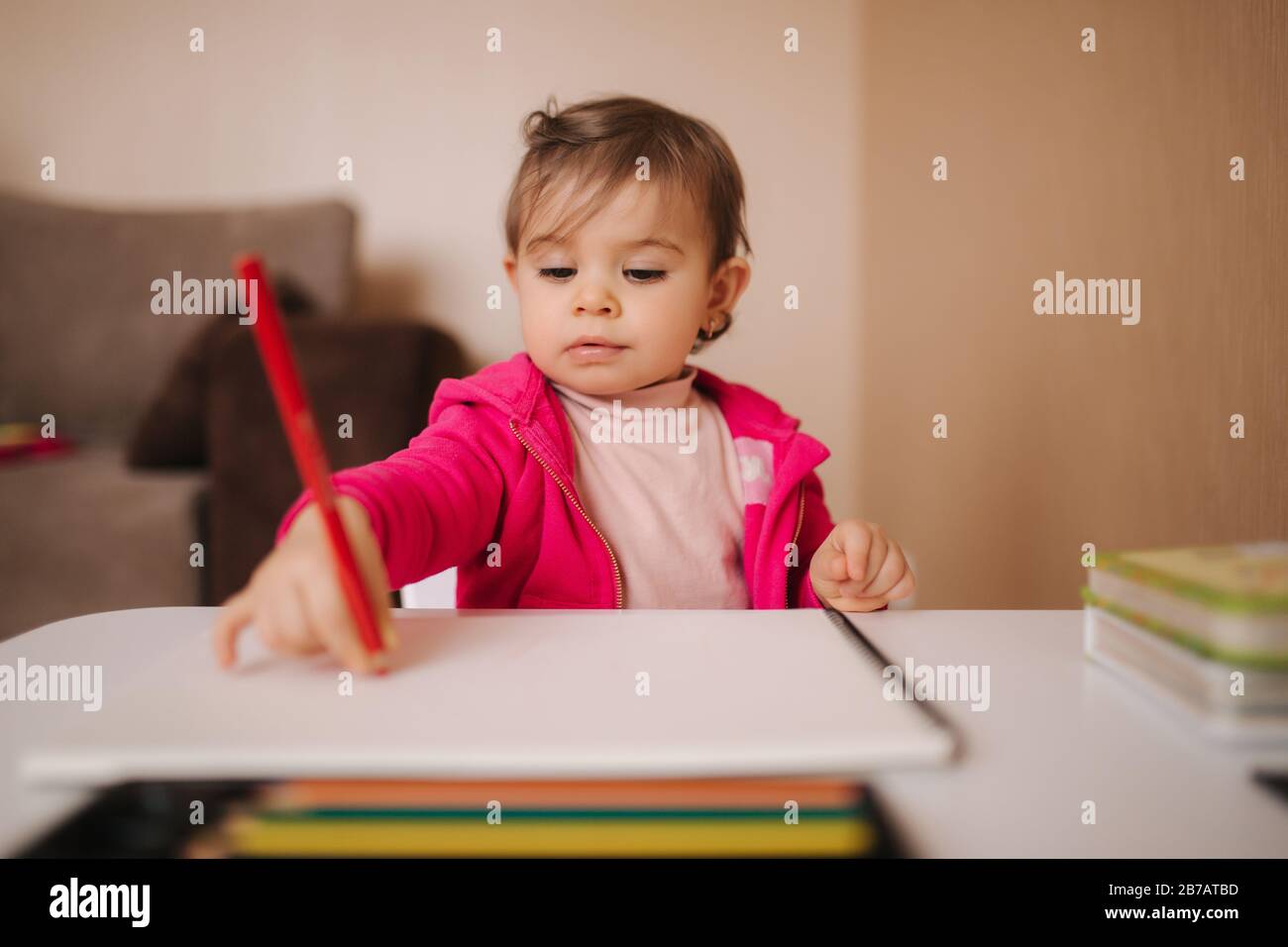 Happy baby girl sit at the table and wthire something. Little girl use ...
