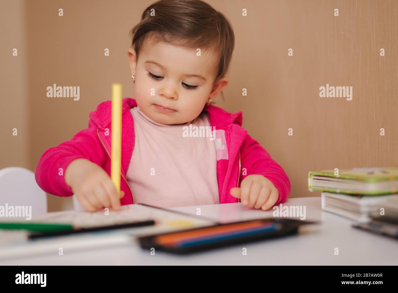 Happy baby girl sit at the table and wthire something. Little girl use ...