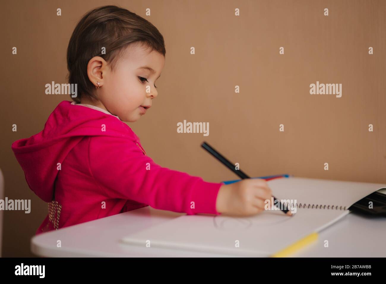 Happy baby girl sit at the table and wthire something. Little girl use ...