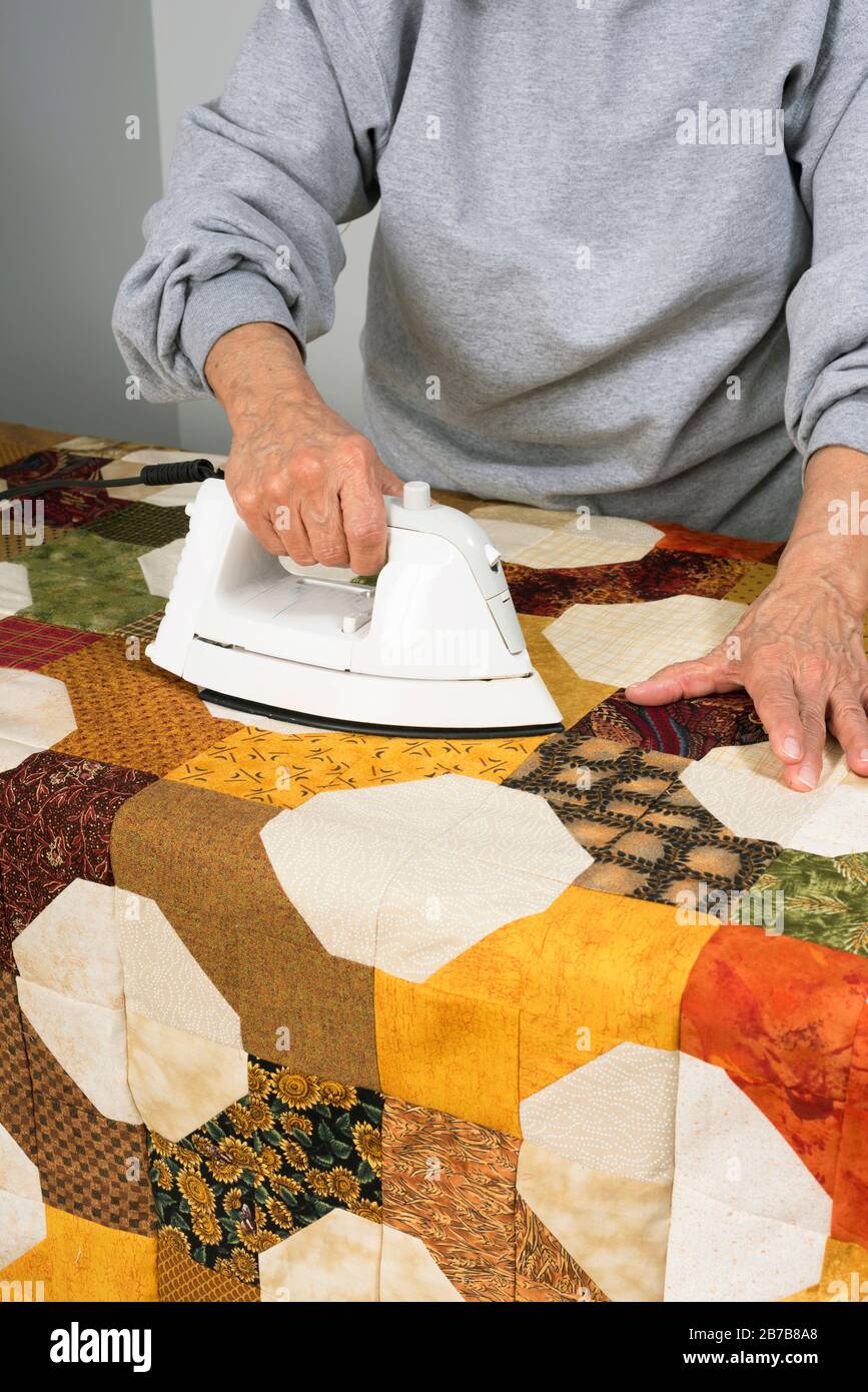 A quilter uses and iron to smooth out any wrinkles om a bow tie quilt ...