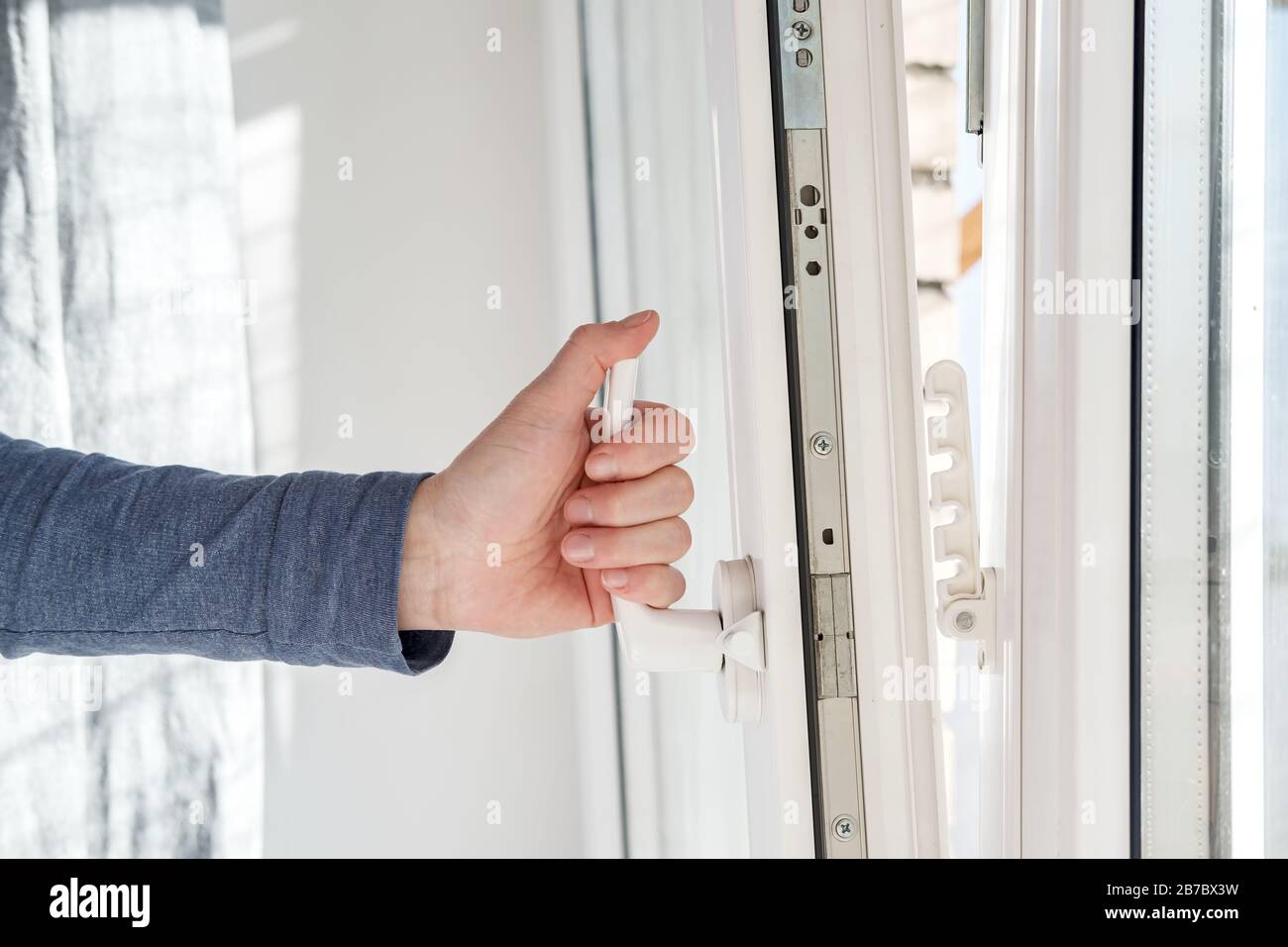 Hand opens a PVC window, holding the handle in an upright position ...