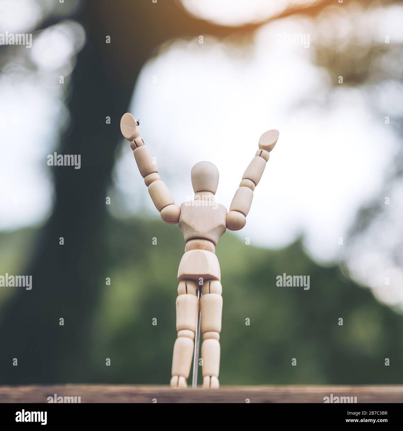 Closeup image of wooden figure model of a man rising hands and standing ...