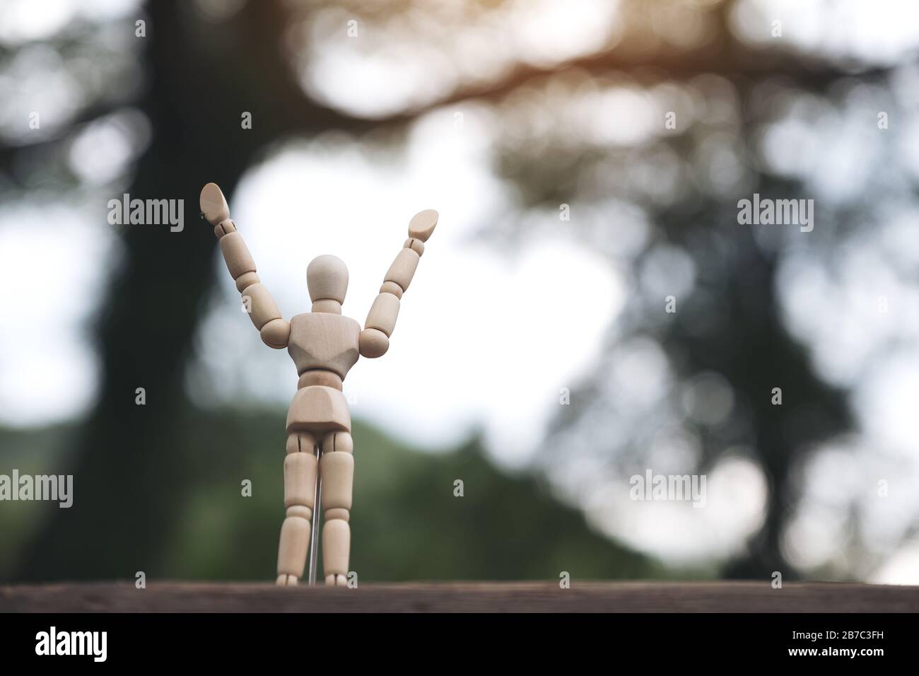 Closeup image of wooden figure model of a man rising hands and standing ...