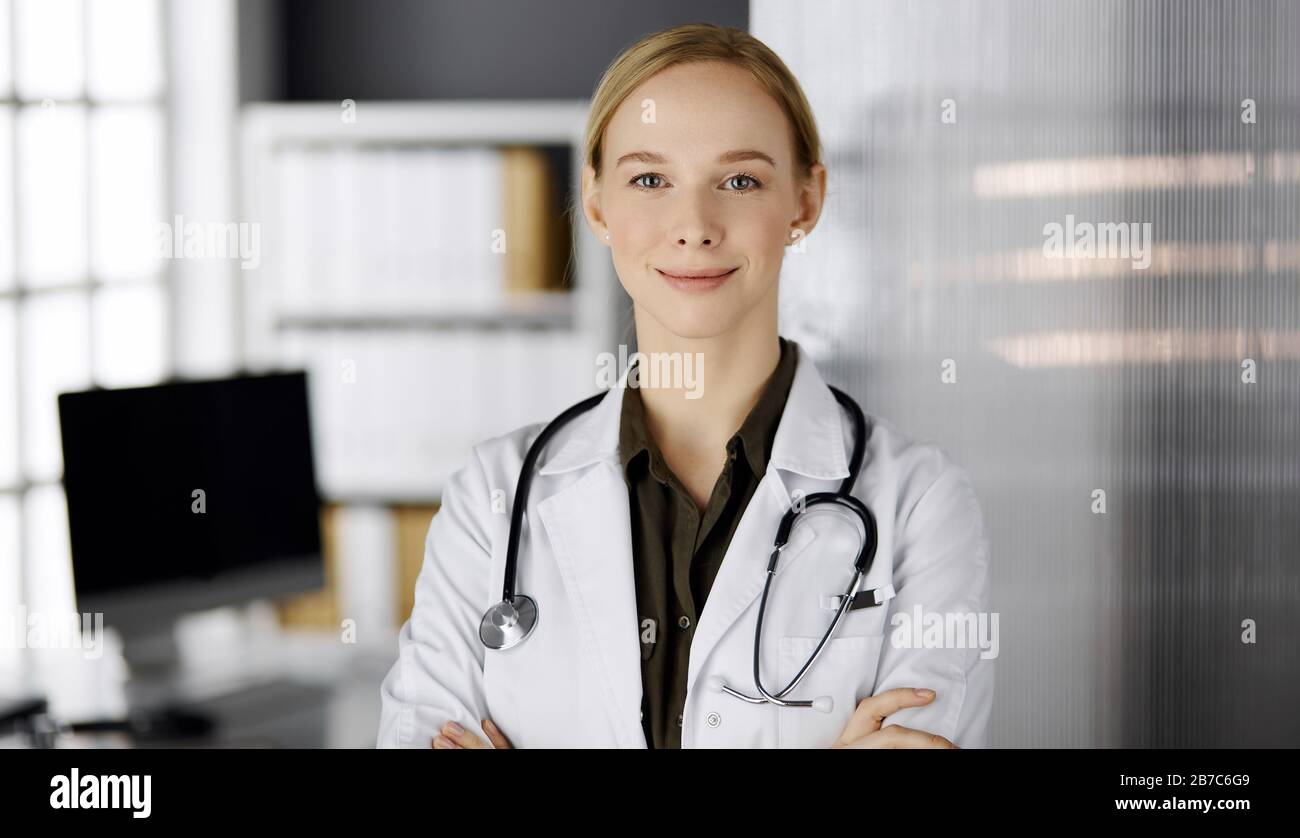 Cheerful smiling female doctor standing in clinic. Portrait of friendly ...
