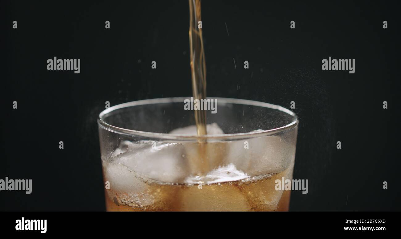 pour cola in glass with ice cubes on black background closeup, wide ...