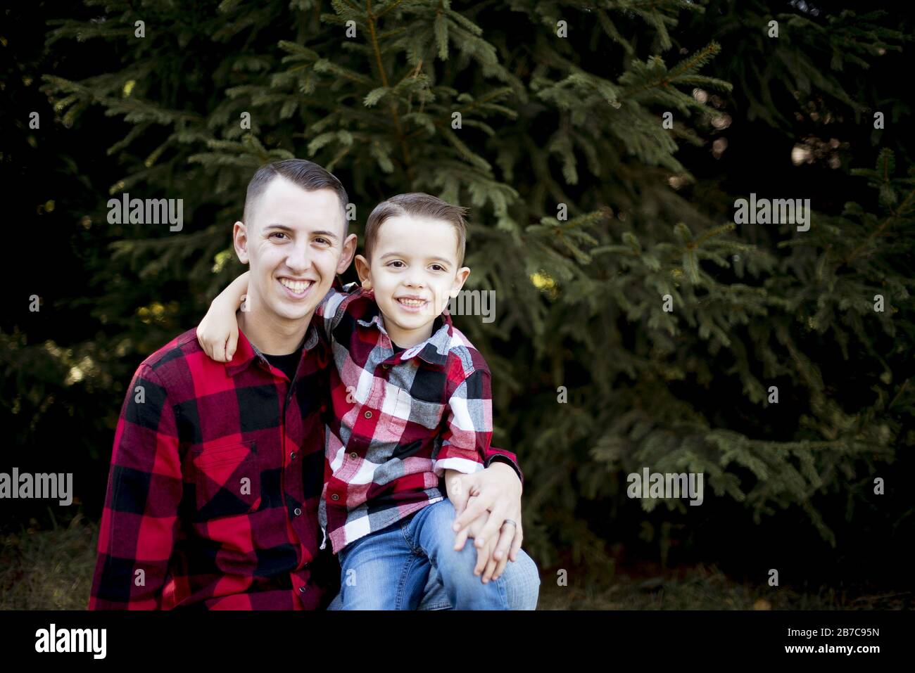 Happy father and son near green fir trees - son sitting on his father's ...