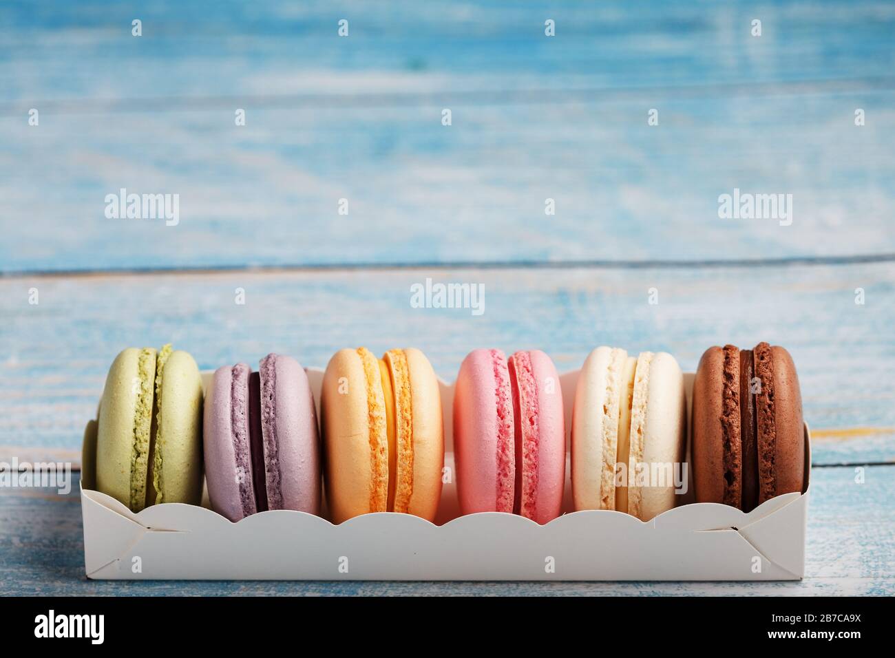 Macaroni cookies of different colors in a box on a blue, old wooden ...